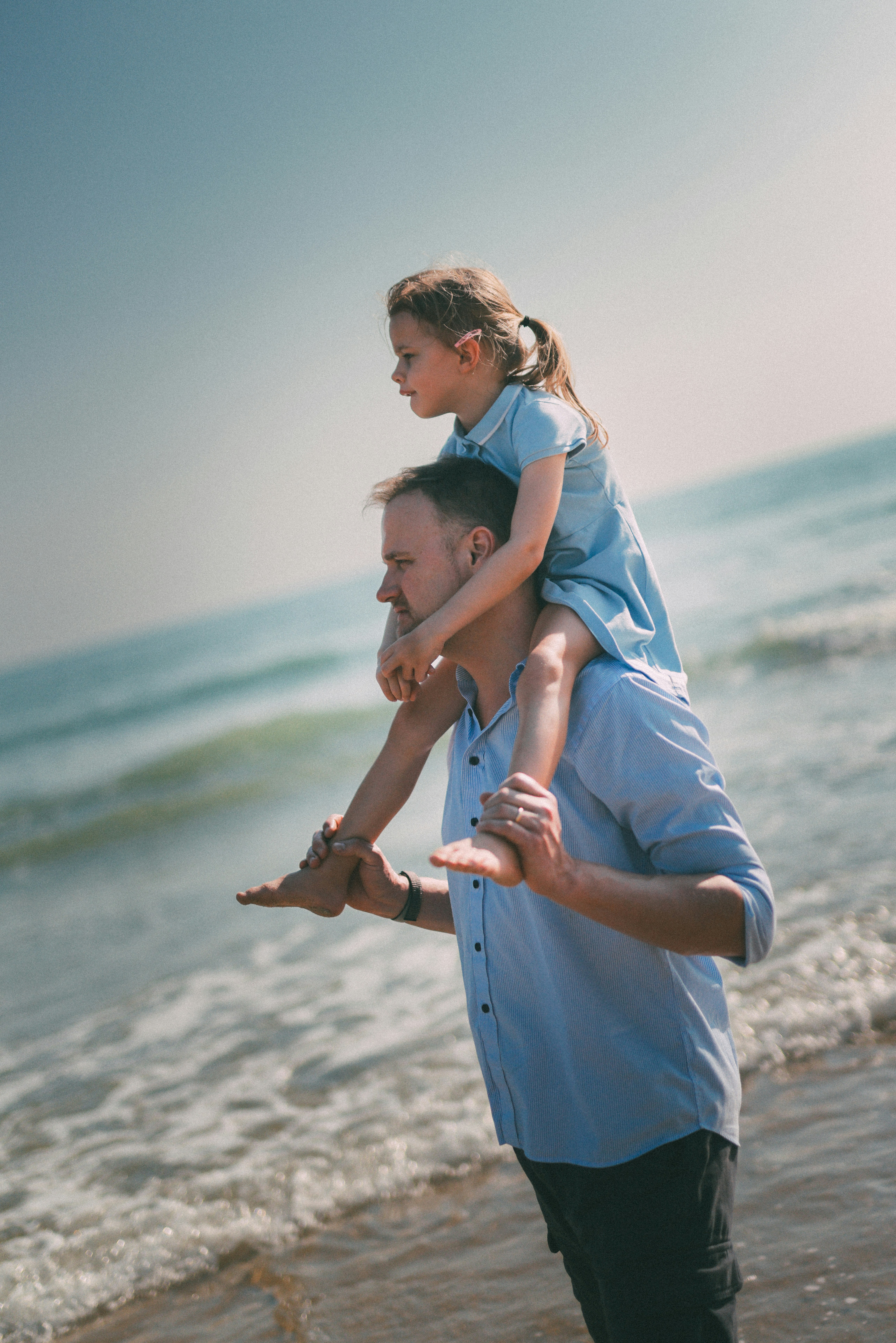 Father and Daughter on Shoulders: A Sunlit Beach Moment