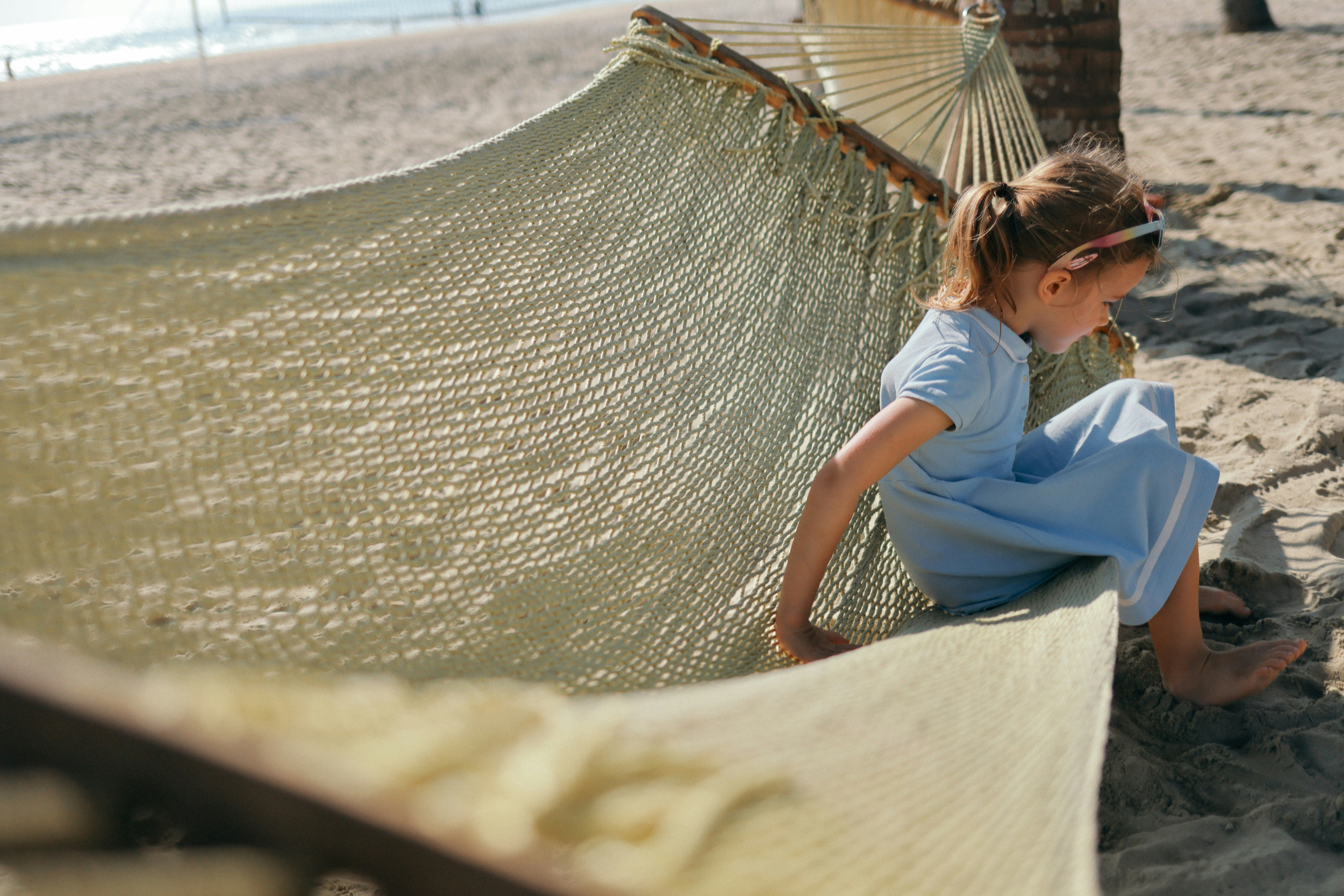 Sunlit Pause: A Young Girl in a Hammock of Beach Light