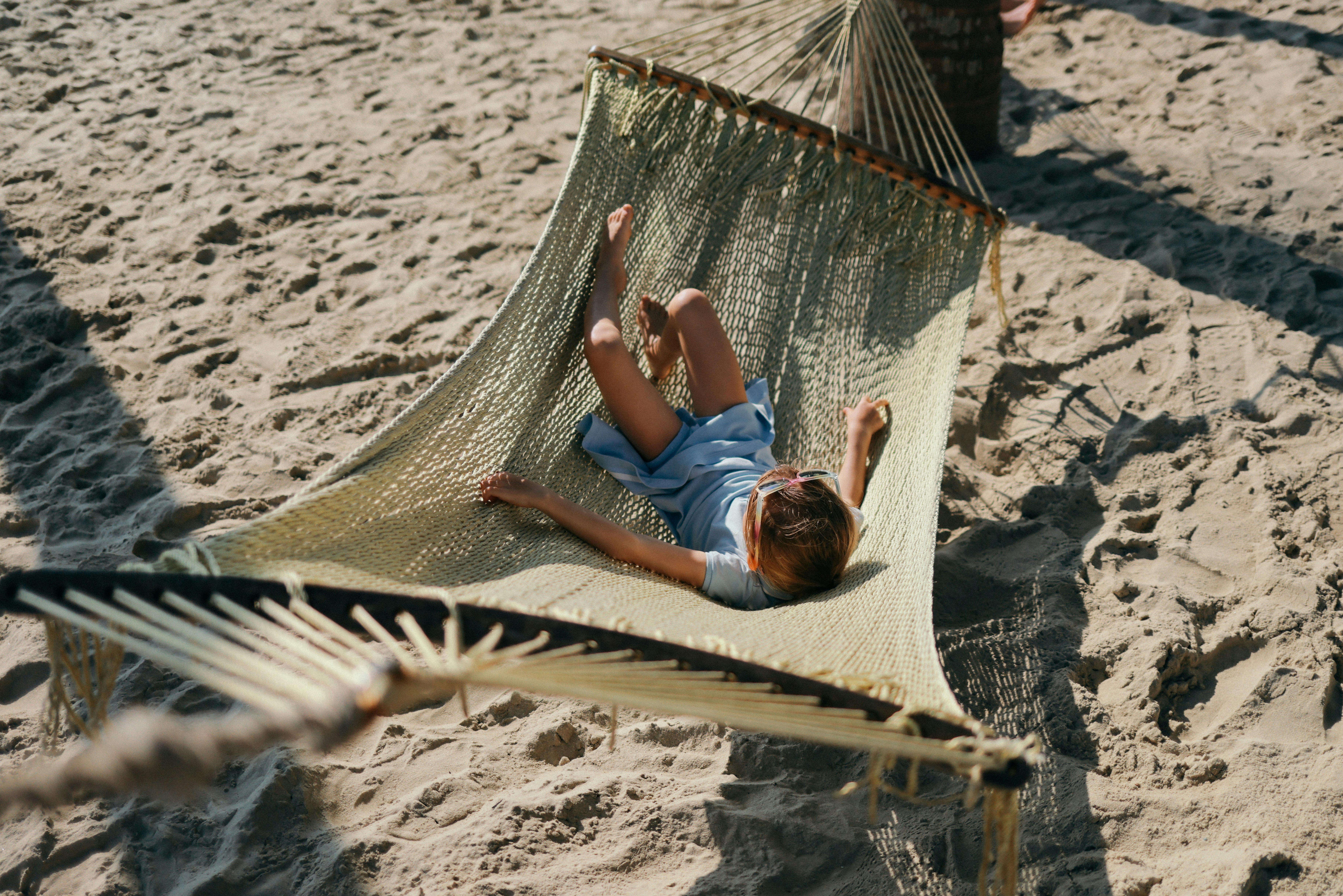 A child relaxes in a hammock on a sandy beach.