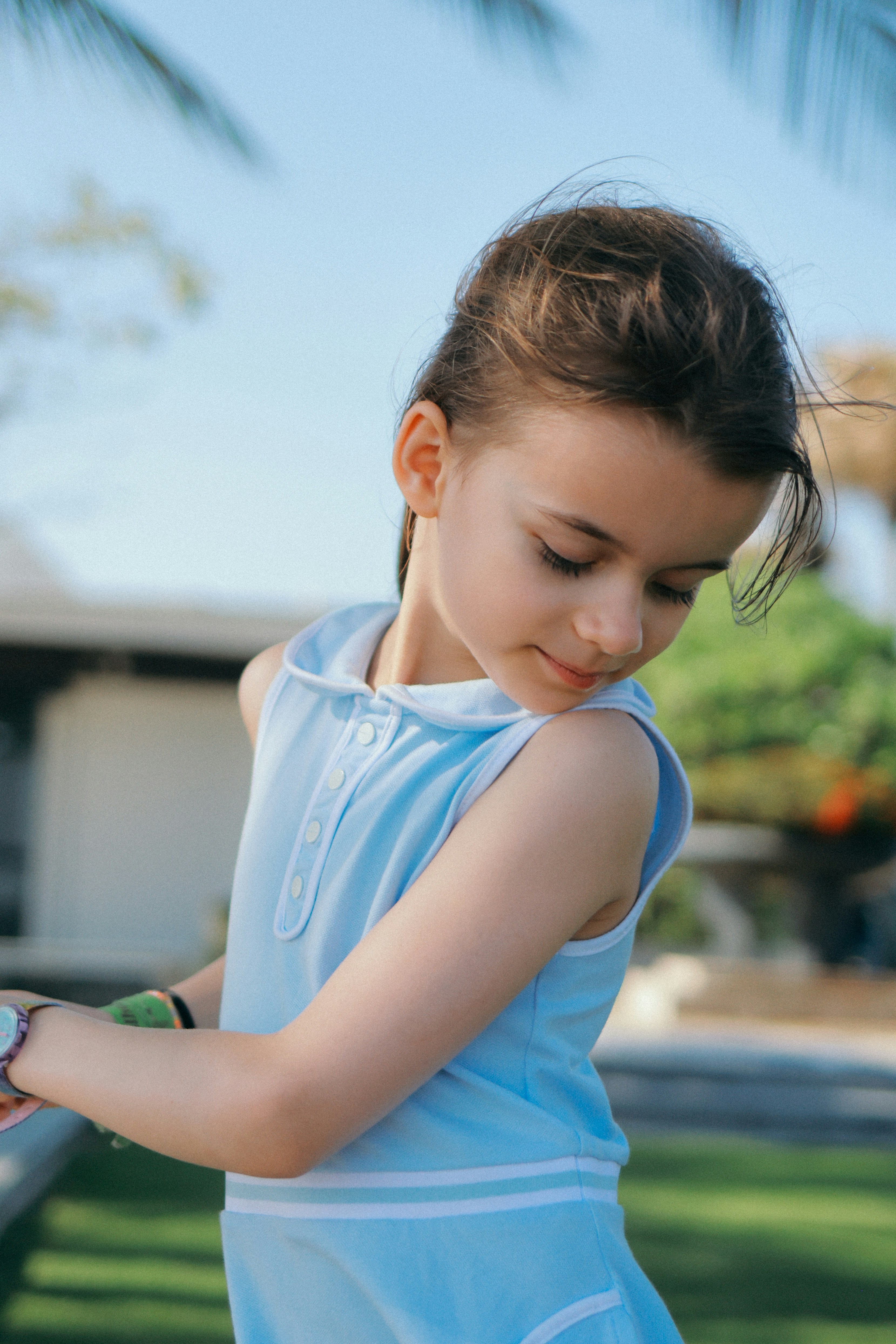 A young girl in a blue dress looks down.