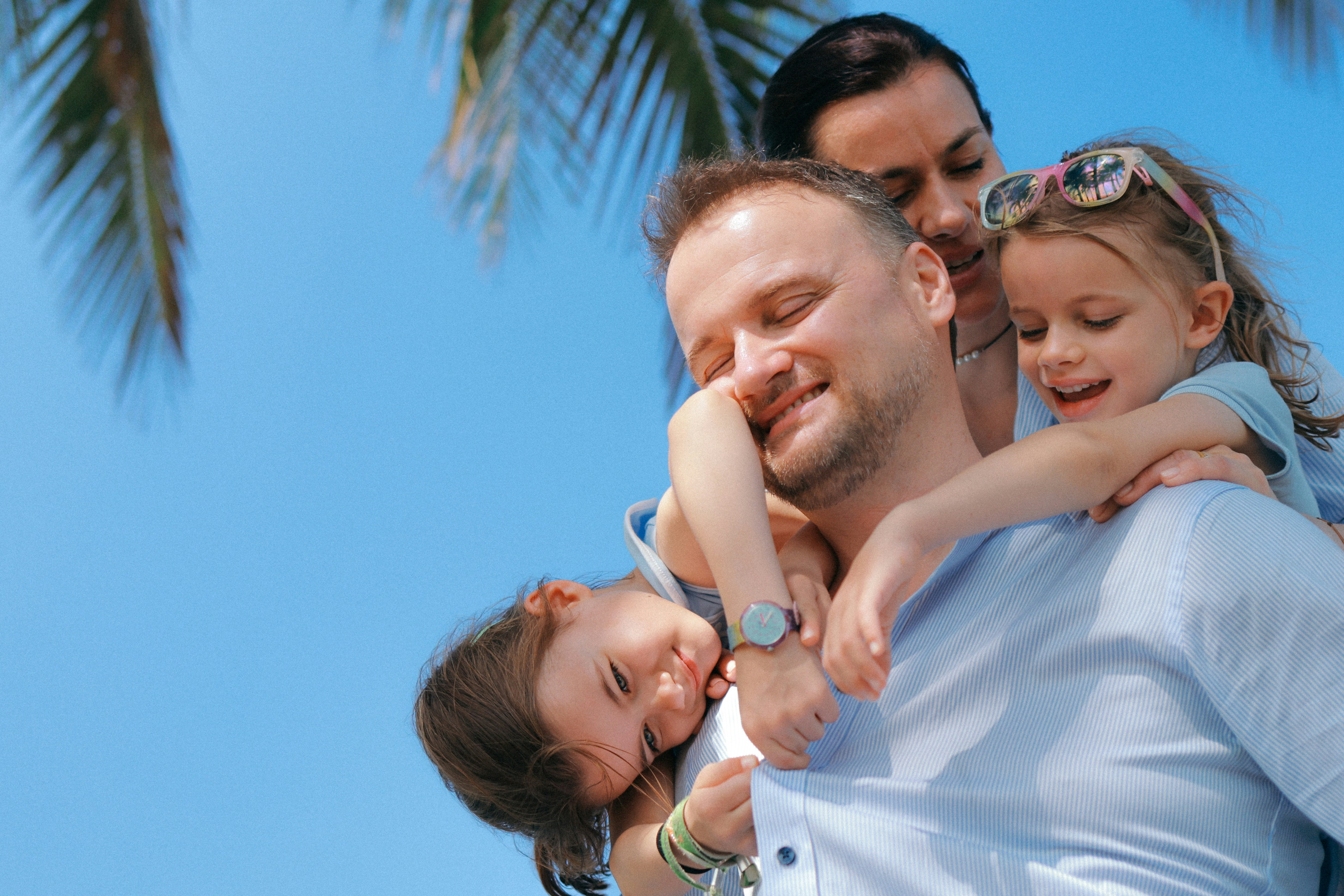 Sunlit family hug under a tropical canopy