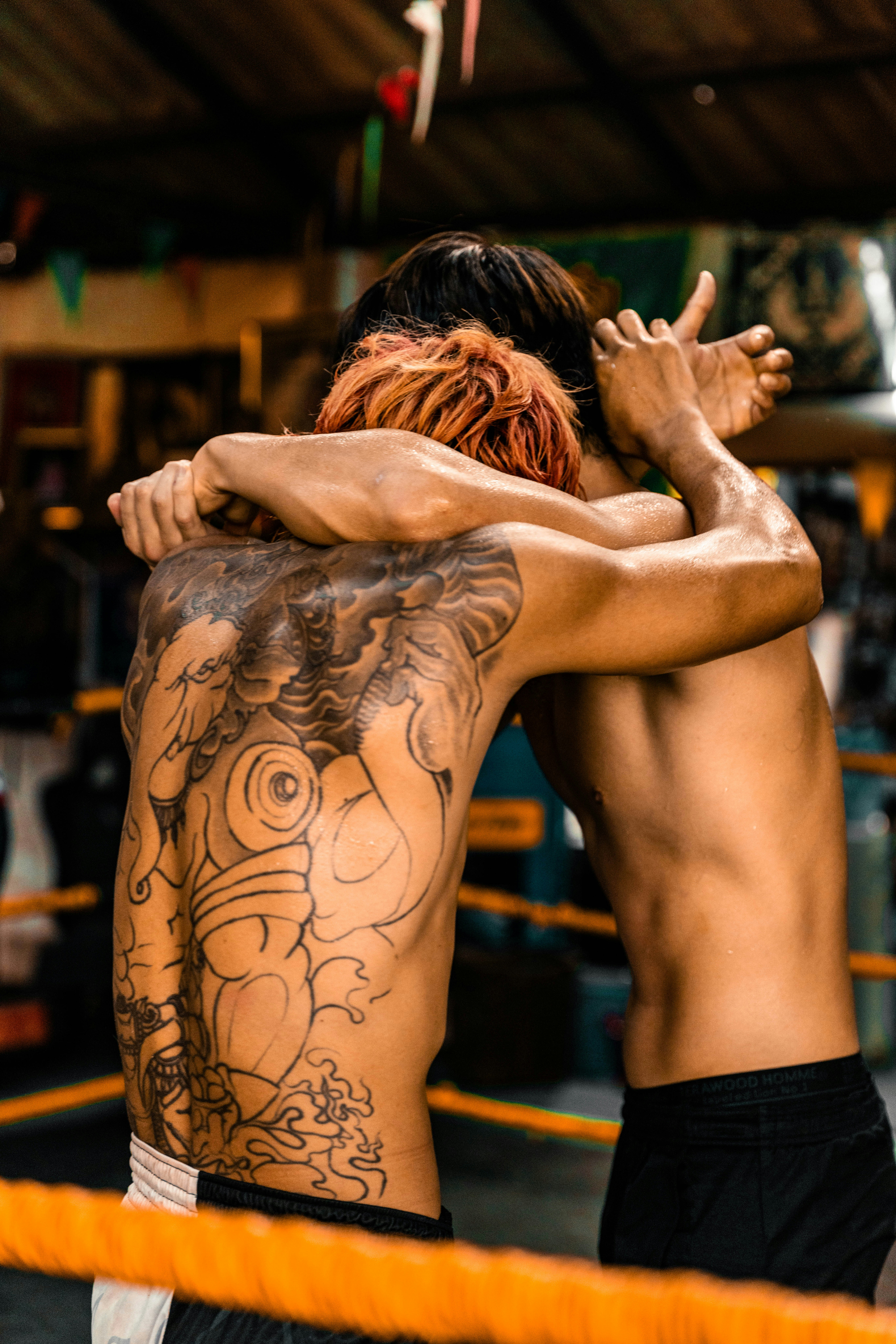 Two Fighters Embrace: Tattooed Back Against a Ring's Glow