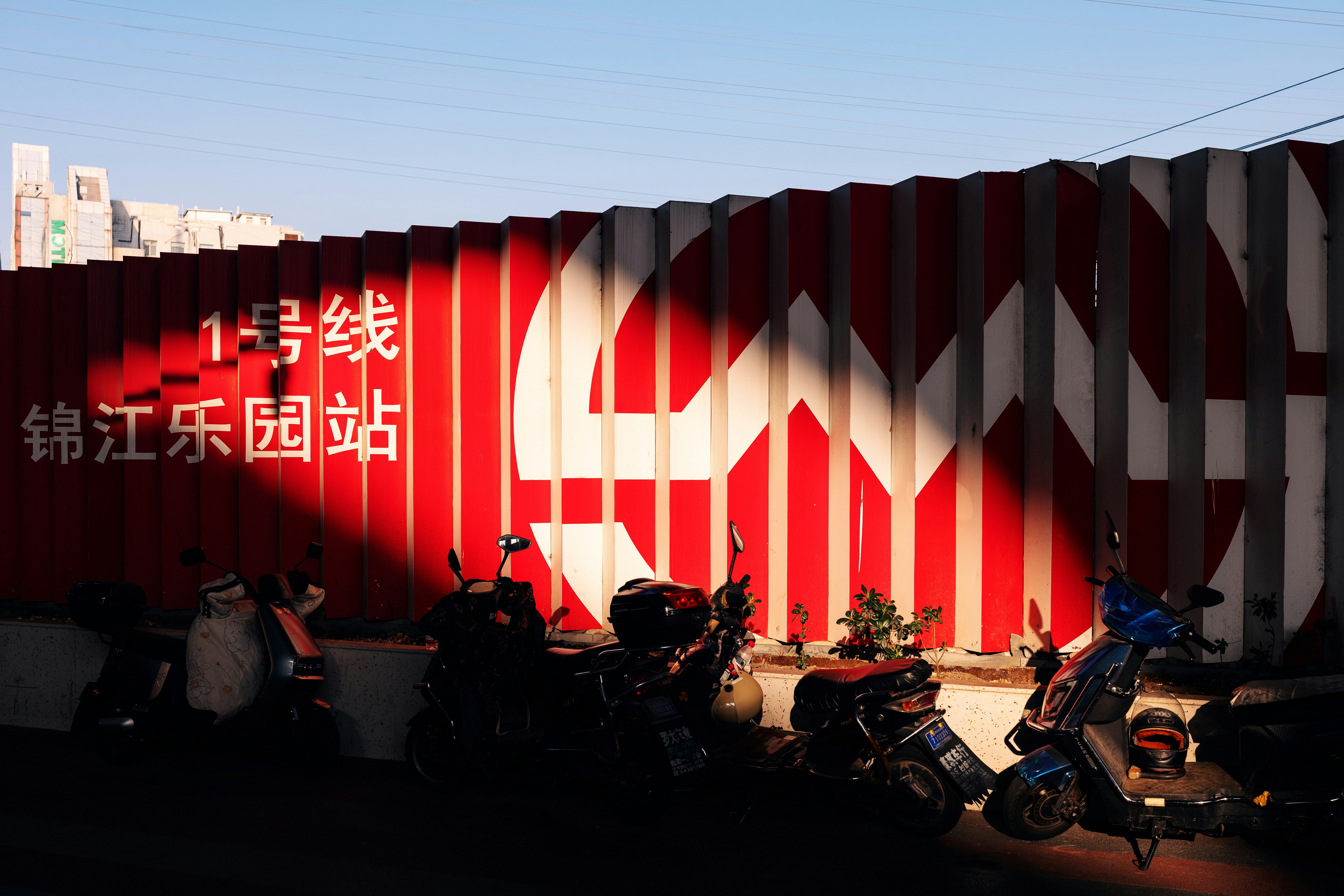 Shadowed scooters line the wall as bold red panels cast geometric shadows