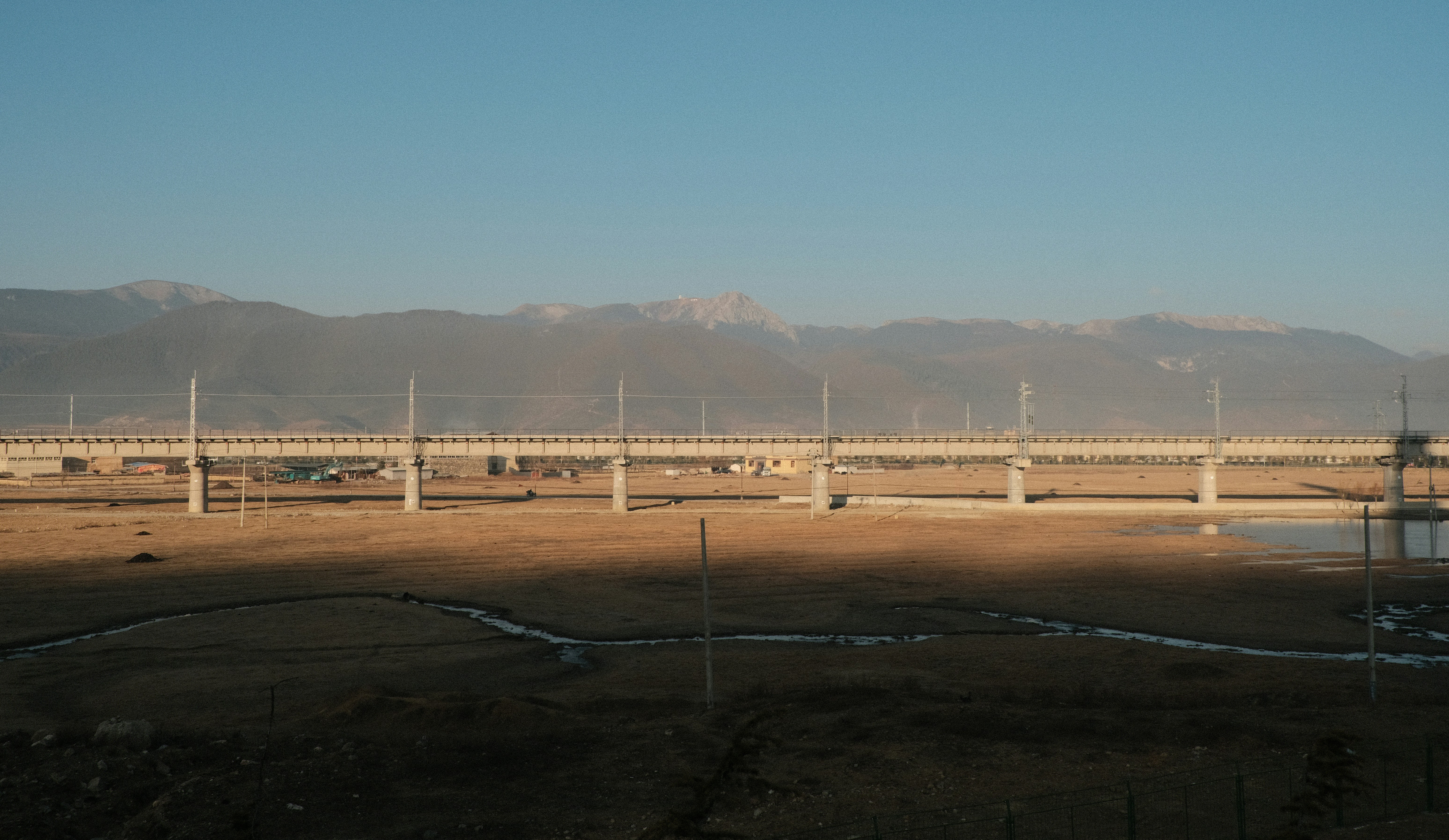 Railway across a desert plain with distant mountains at dusk
