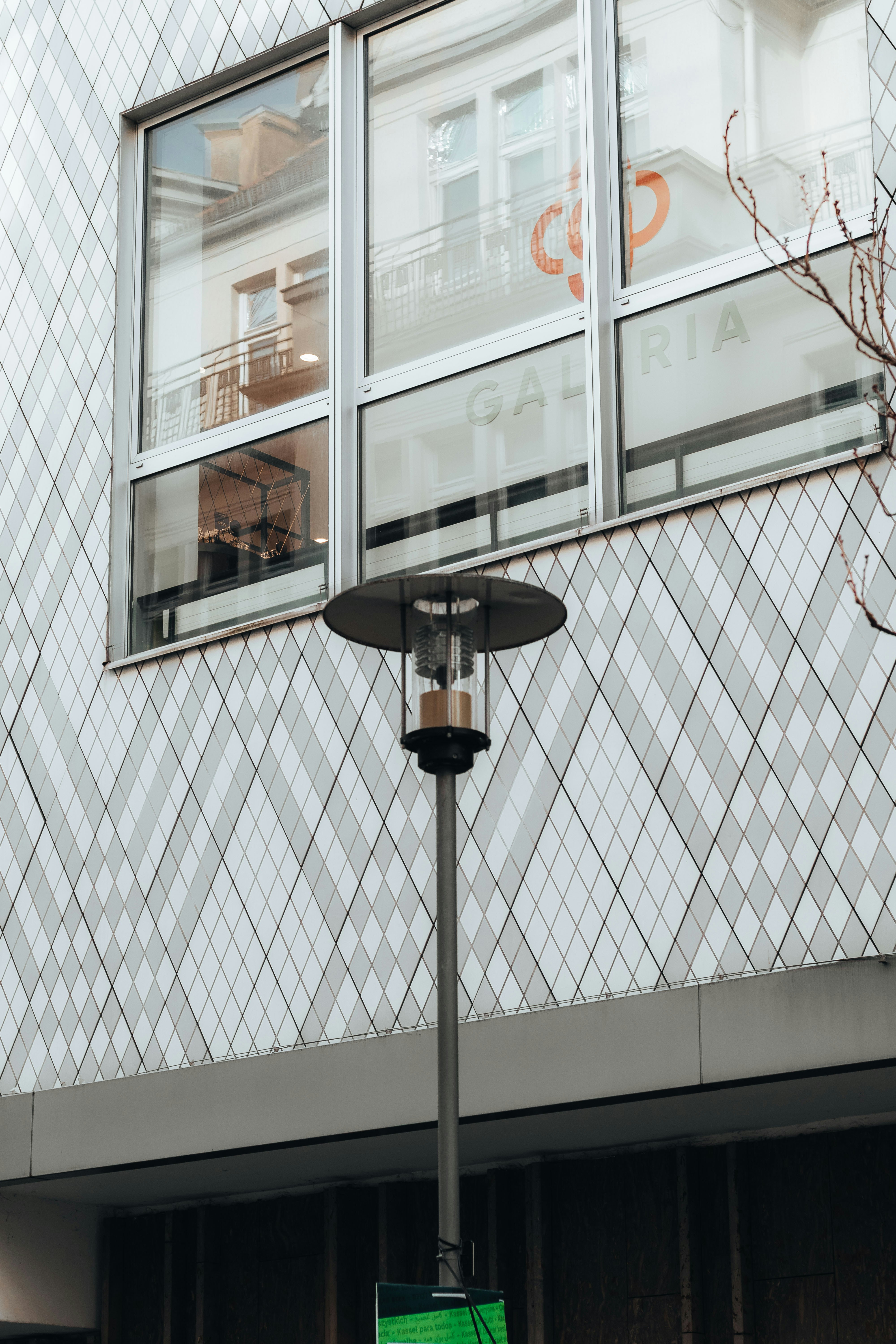 Architectural facade with diamond-pattern tiles and a central streetlamp, captured in daylight to emphasize geometry and urban texture.