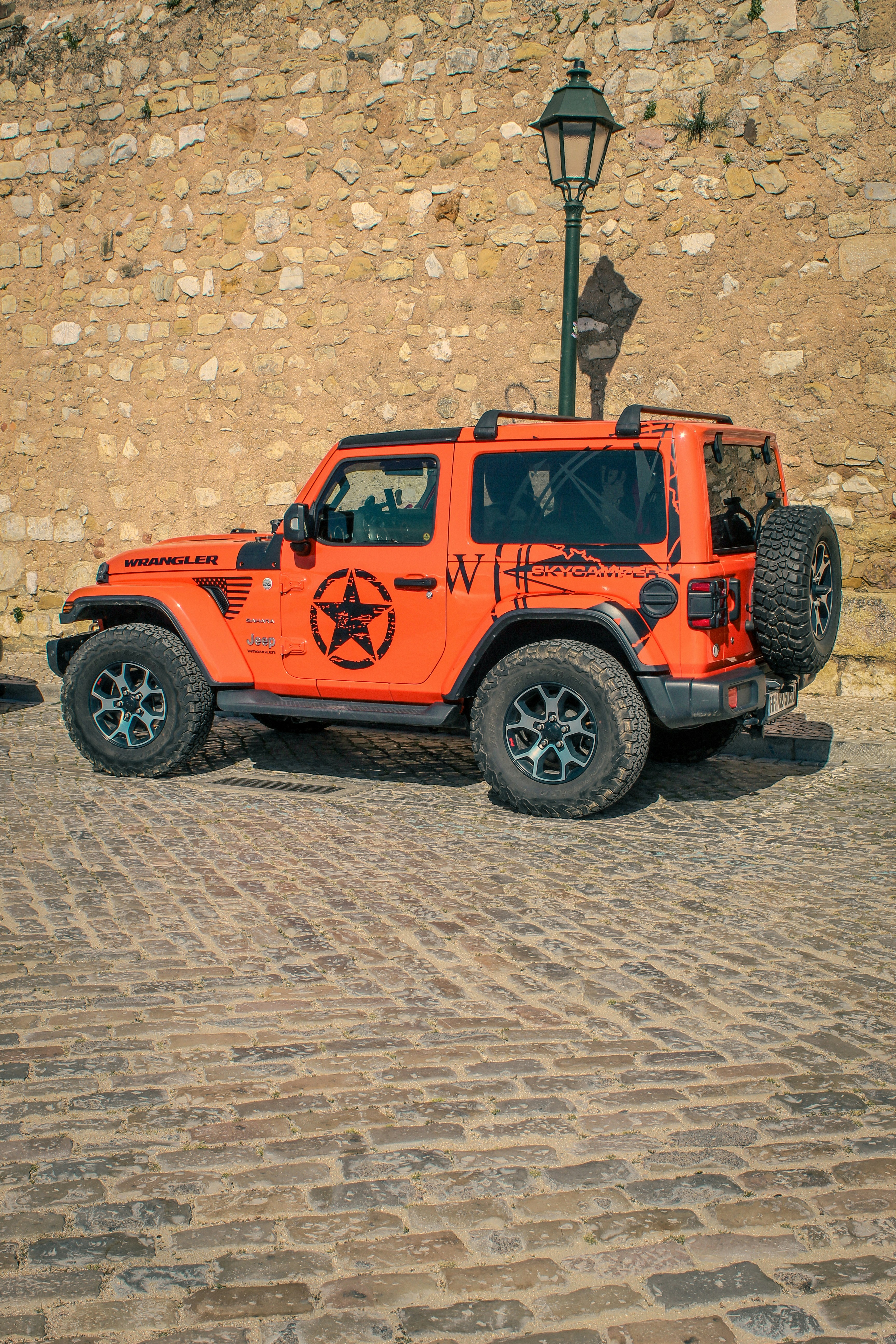 Orange Wrangler Resting Against a Cobblestone Street with Stone Wall Backdrop