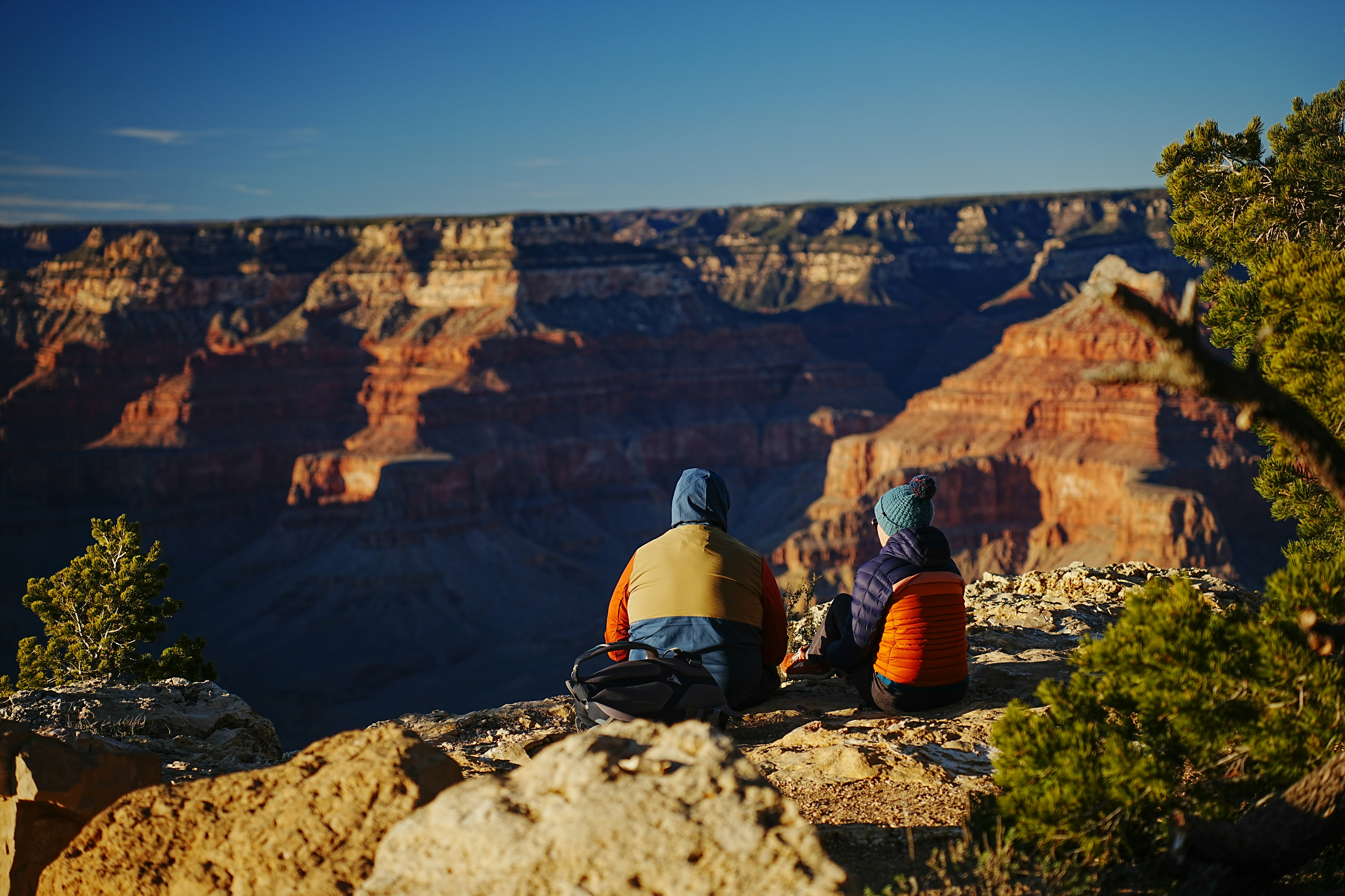 Two hikers at the edge of the Grand Canyon watching the canyon glow at sunset