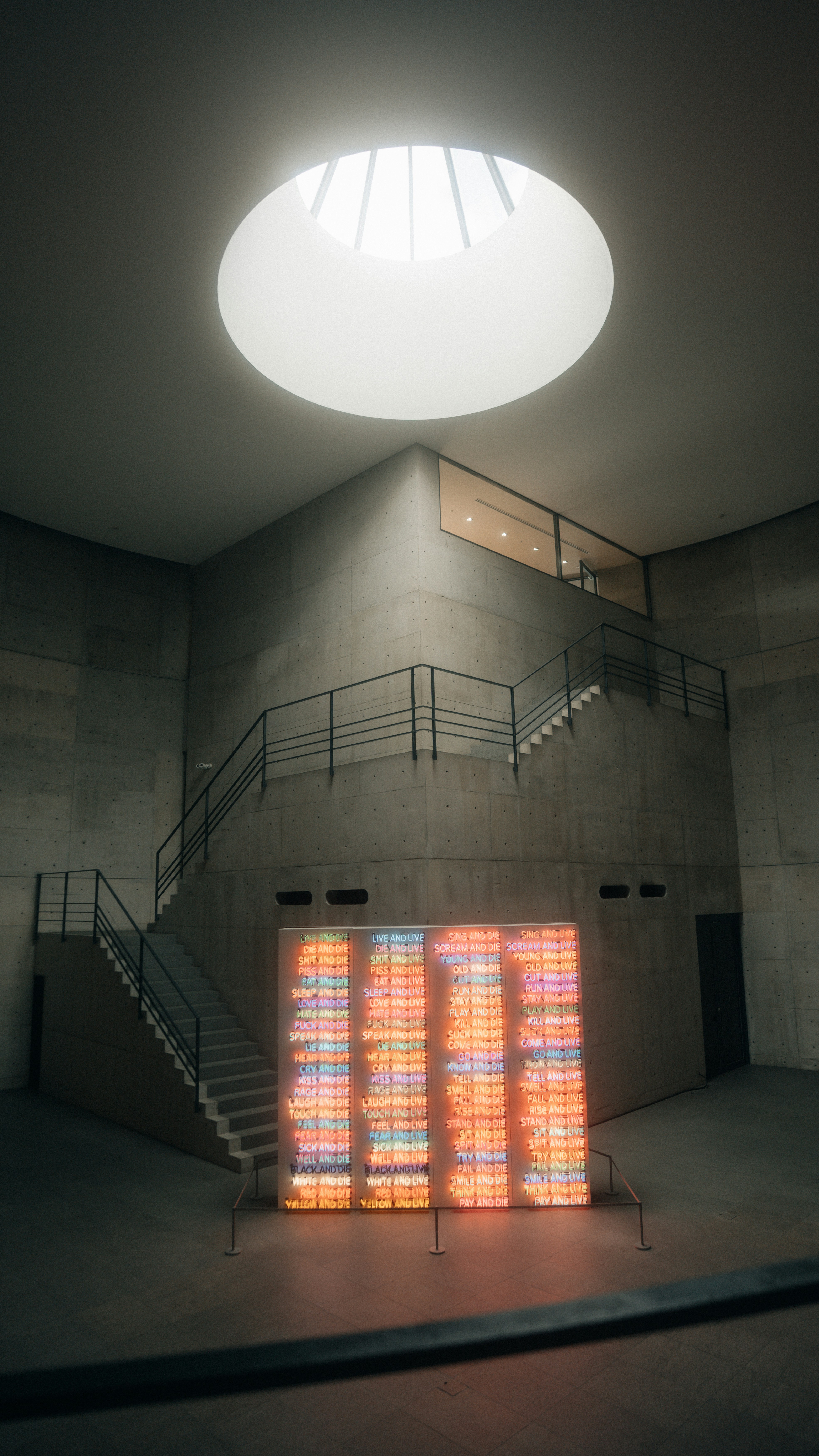 Circular skylight over brutalist stairs with neon sculpture glow