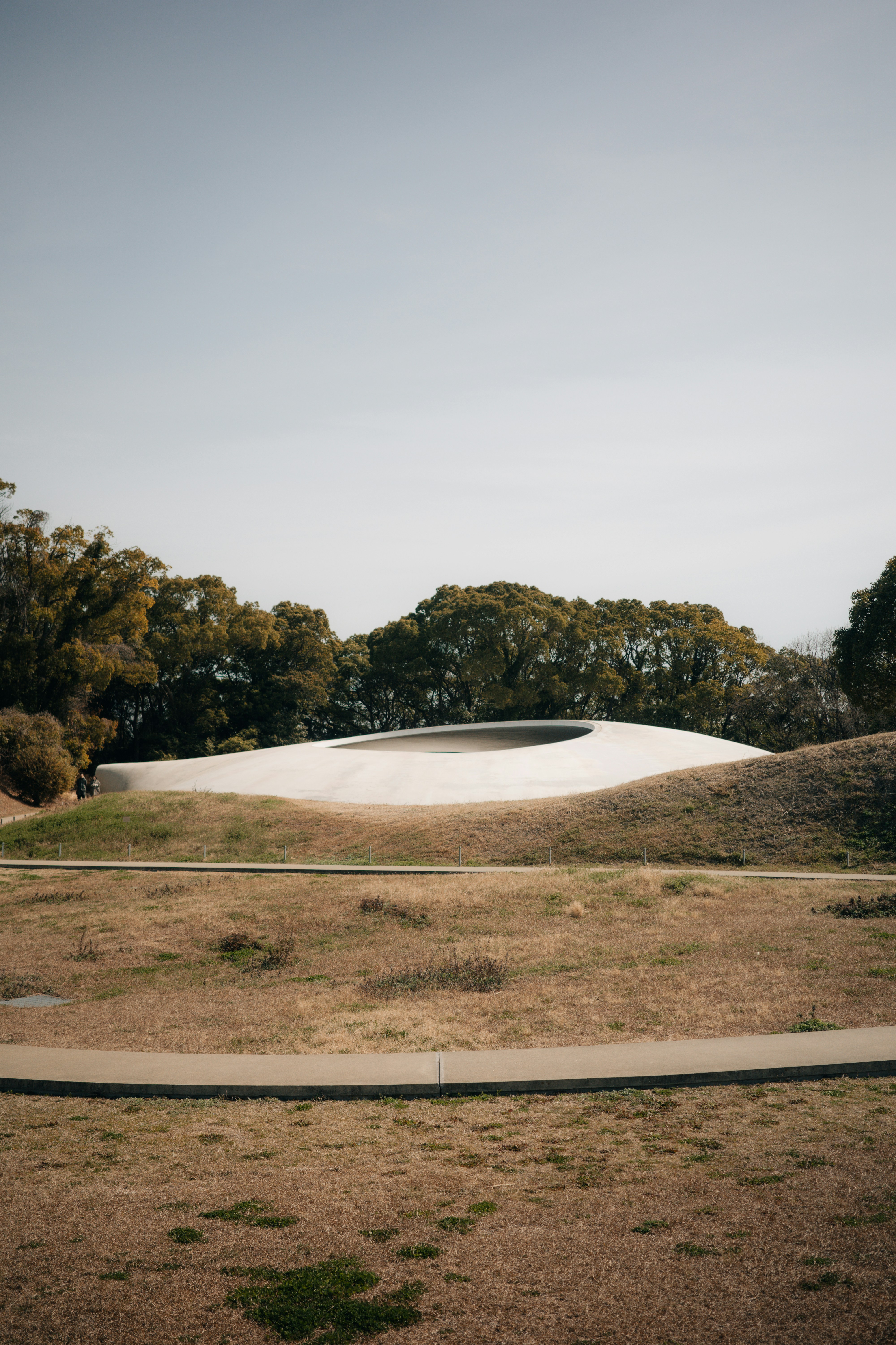 White U-shaped pavilion rises from a gentle hill under a clear sky