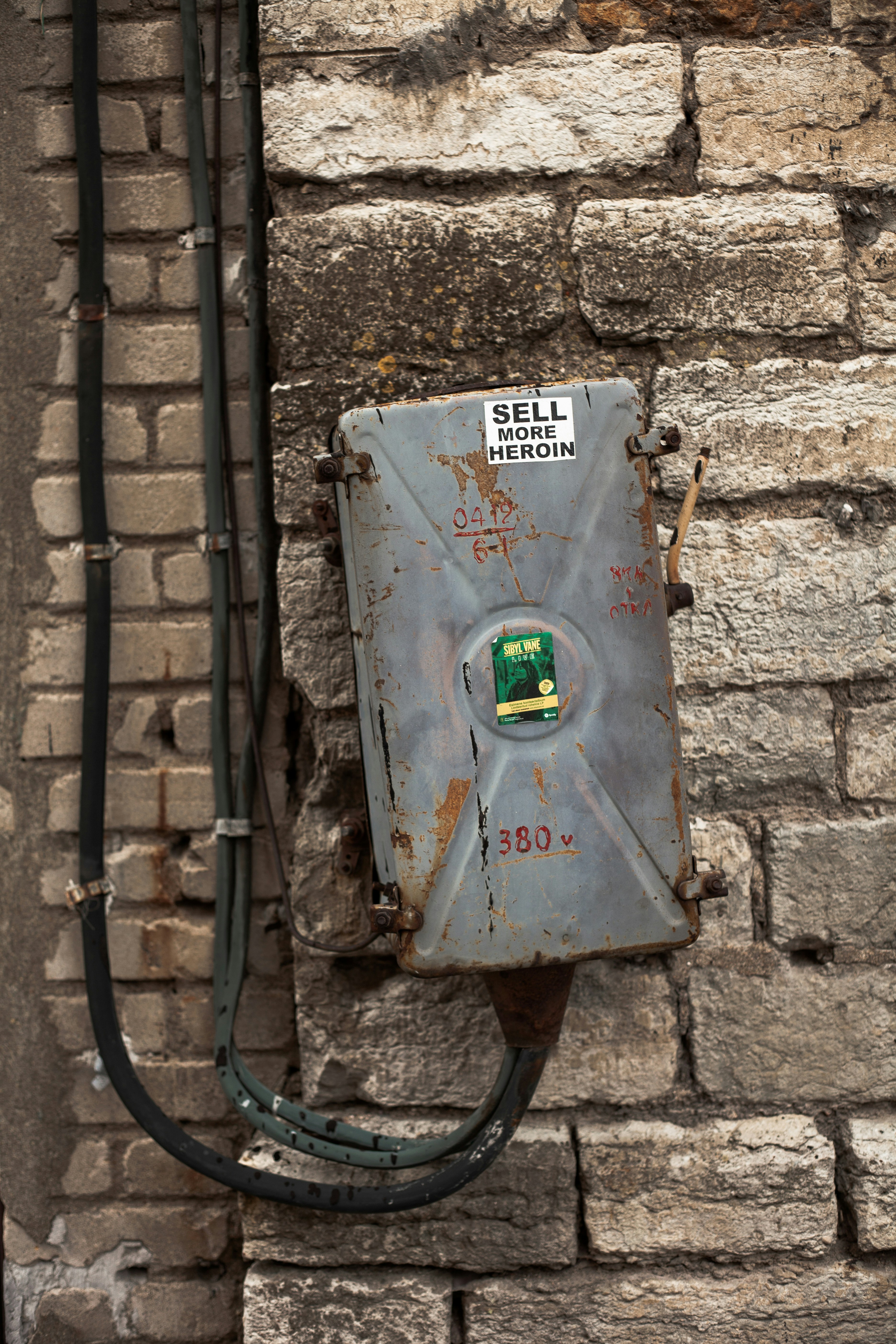 Weathered Utility Box with 'Sell More Heroin' Sign on a Rustic Stone Wall