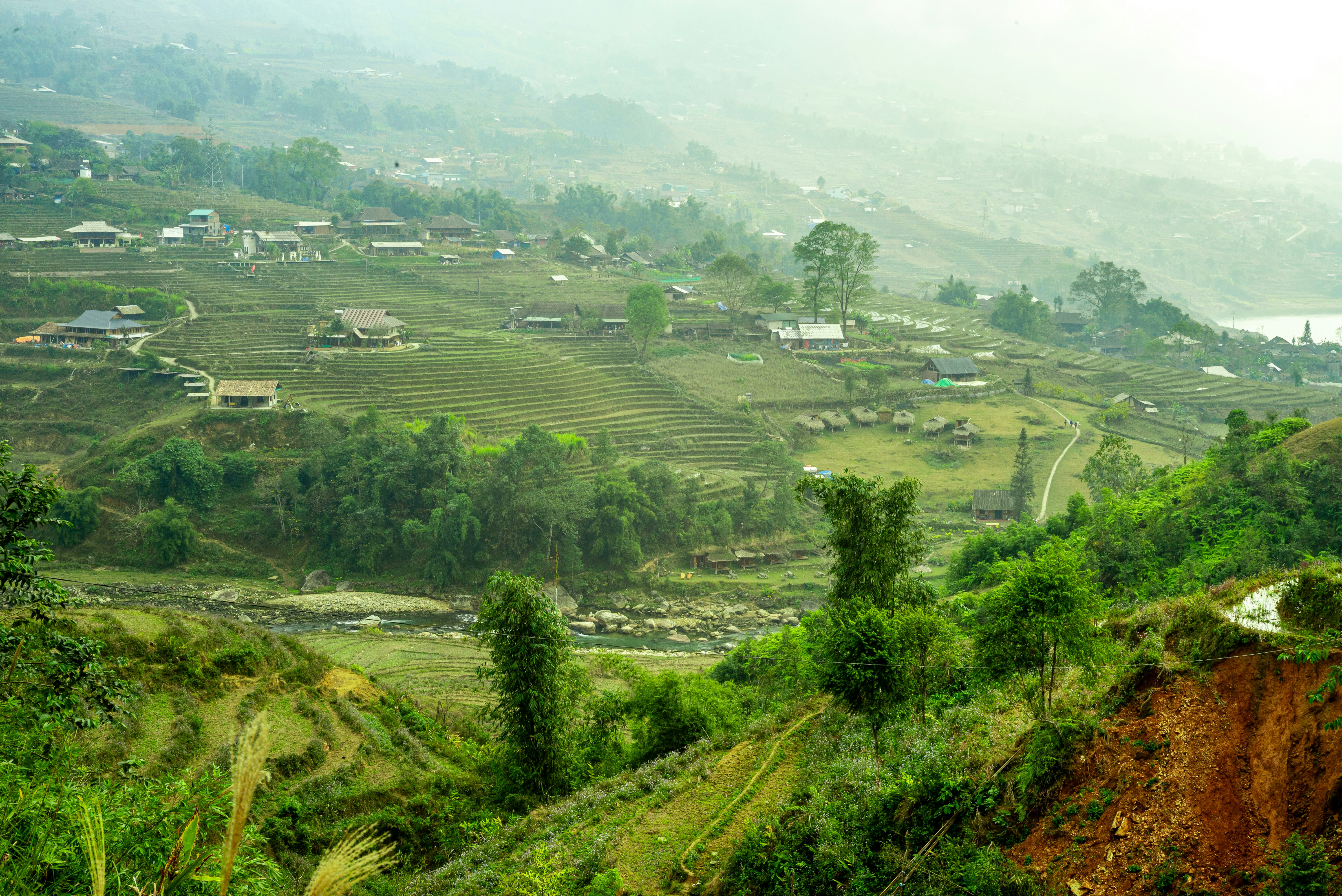 Green terraced hills with small village and misty mountains.