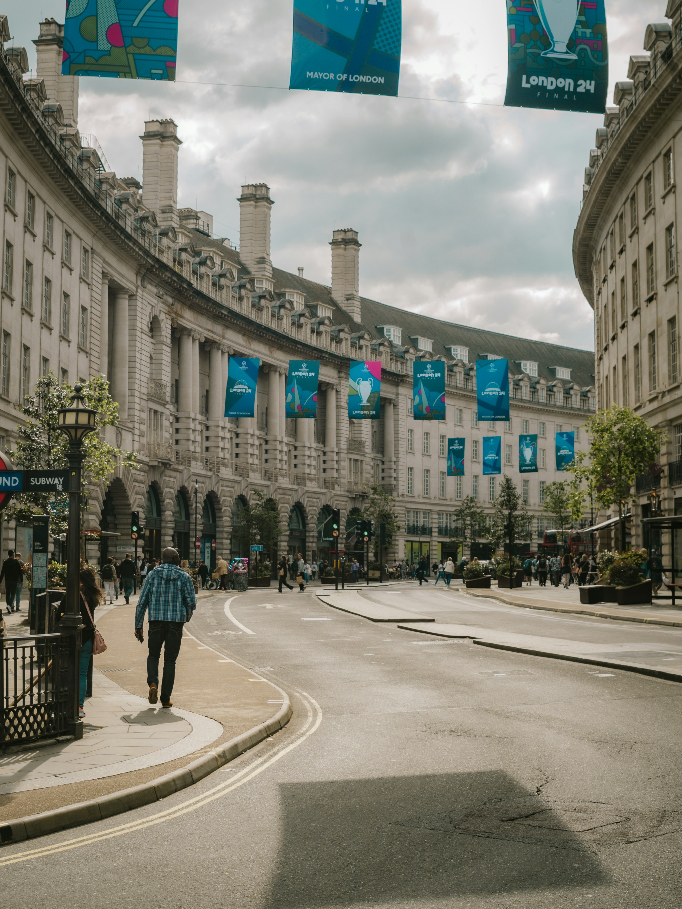 Blue banners drape a grand London arcade as pedestrians traverse the curved street