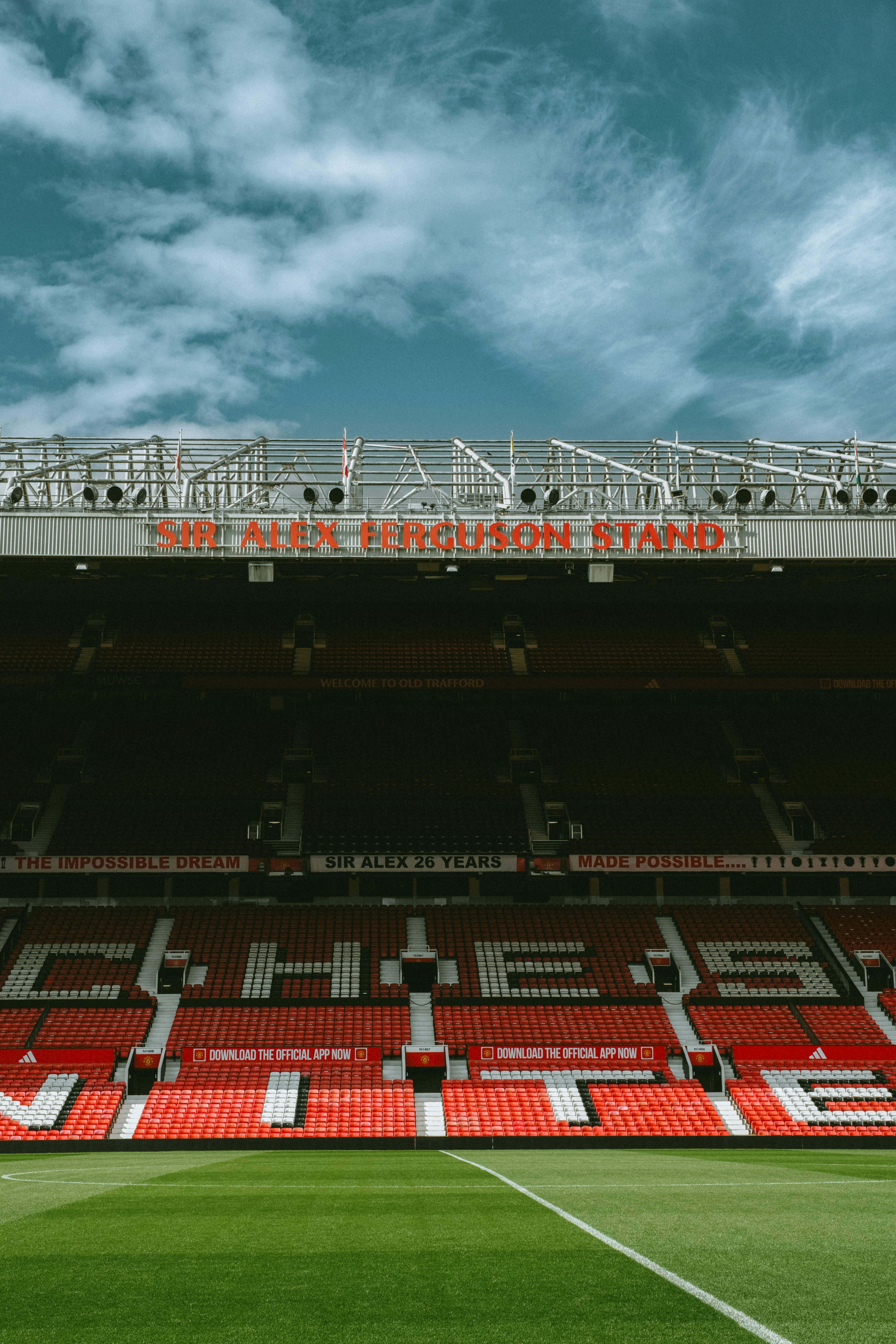 Sir Alex Ferguson Stand: Red Seats and Green Pitch Under a Broad Sky