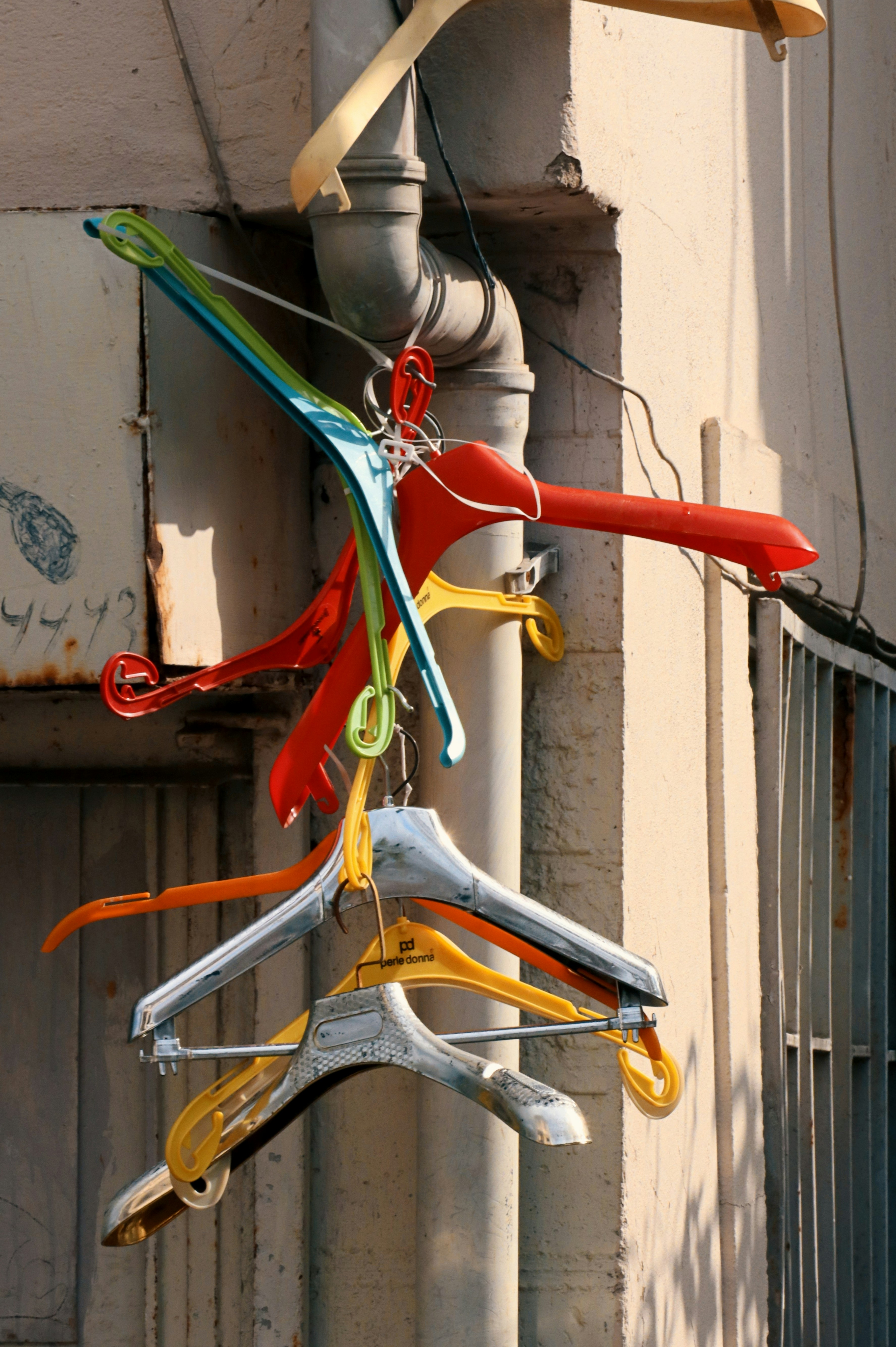 Colorful clotheslines of utility: a vertical tangle of hangers against a sunlit wall