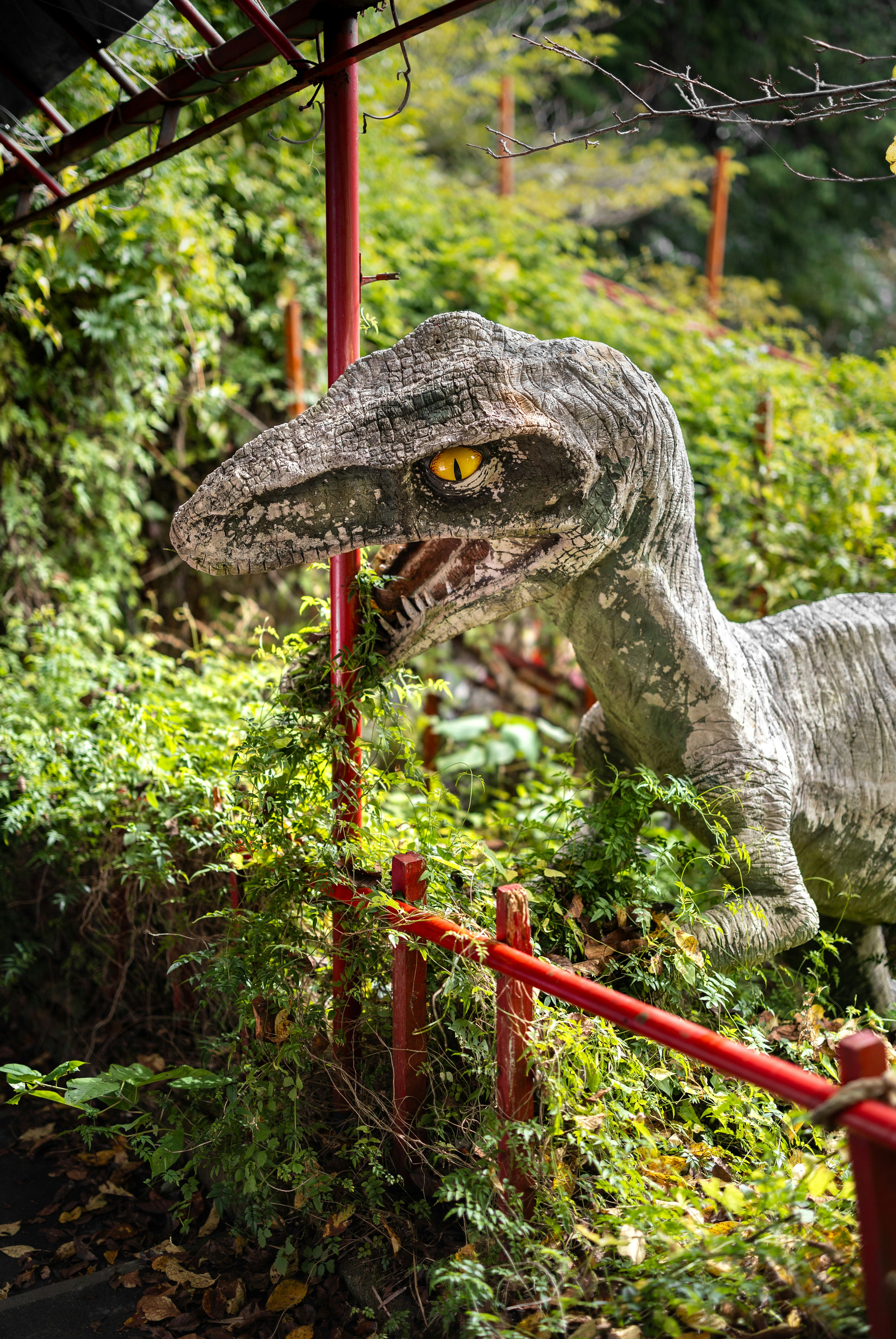 A dinosaur statue stands among lush green foliage.