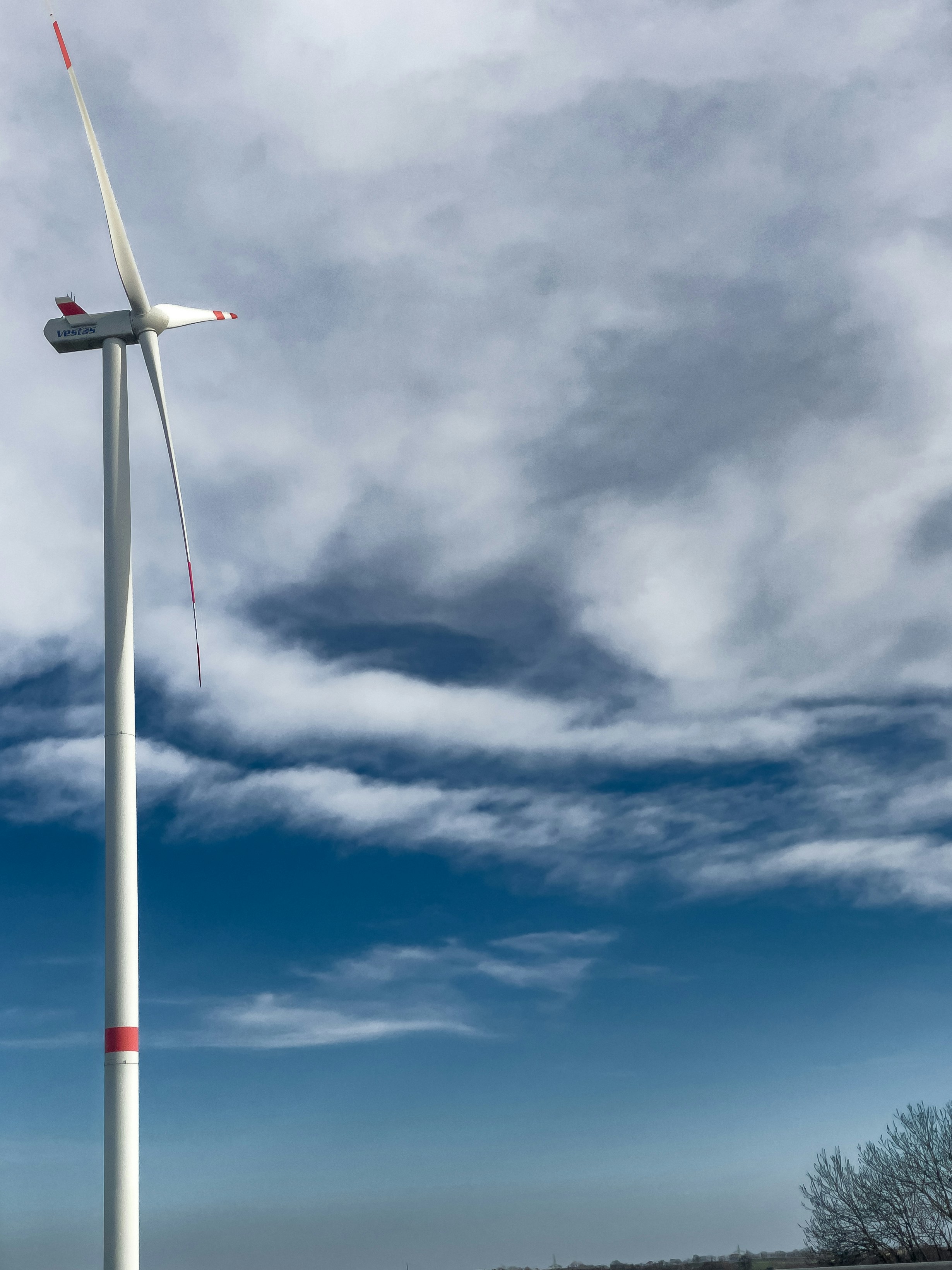 A lone wind turbine stands against a cloudy blue sky.