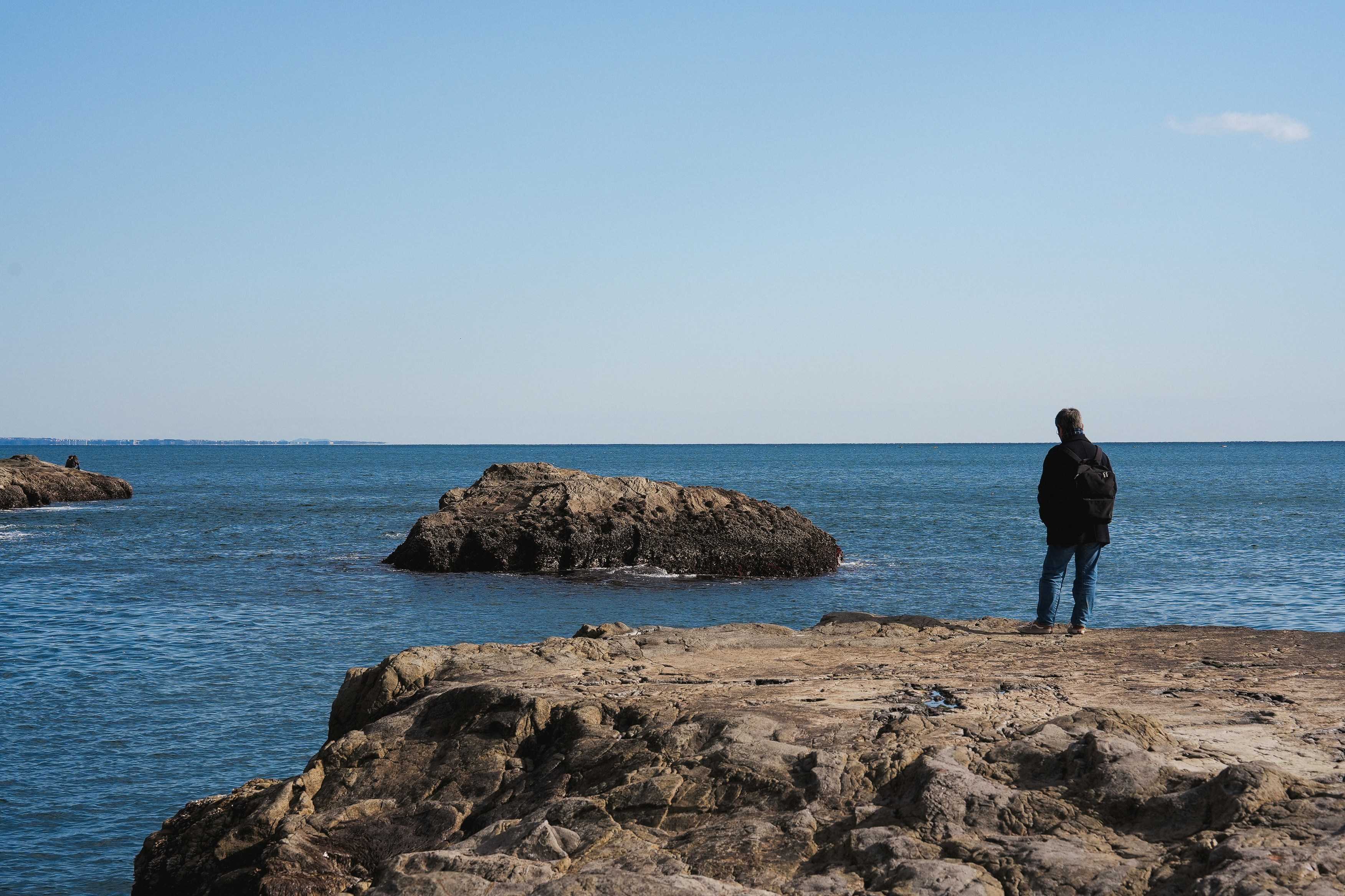  solitary figure on coastal rock under a clear sky
