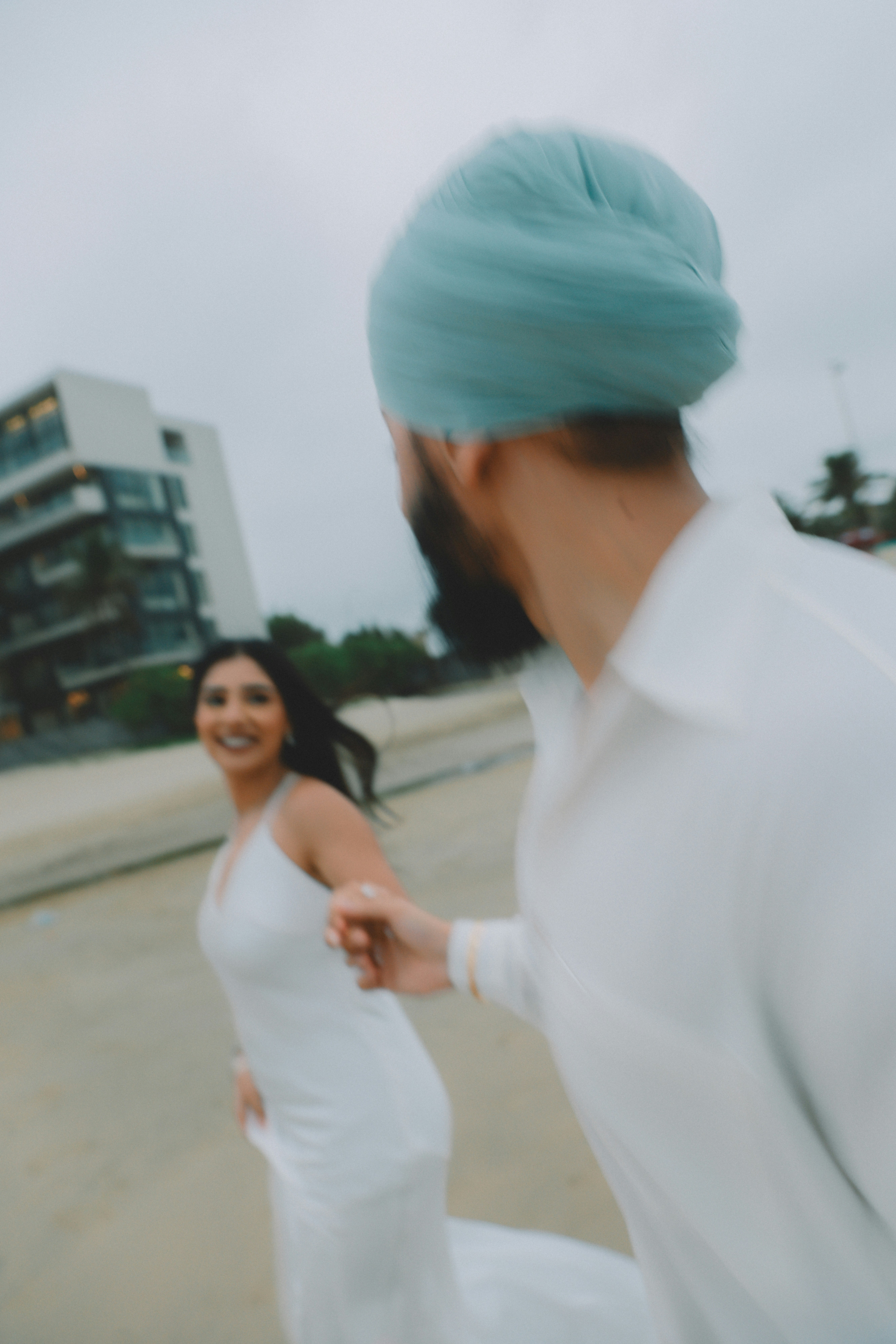 Blurry Beachfront Moment: A Man in a Turquoise Turban Reaches for a Smile
