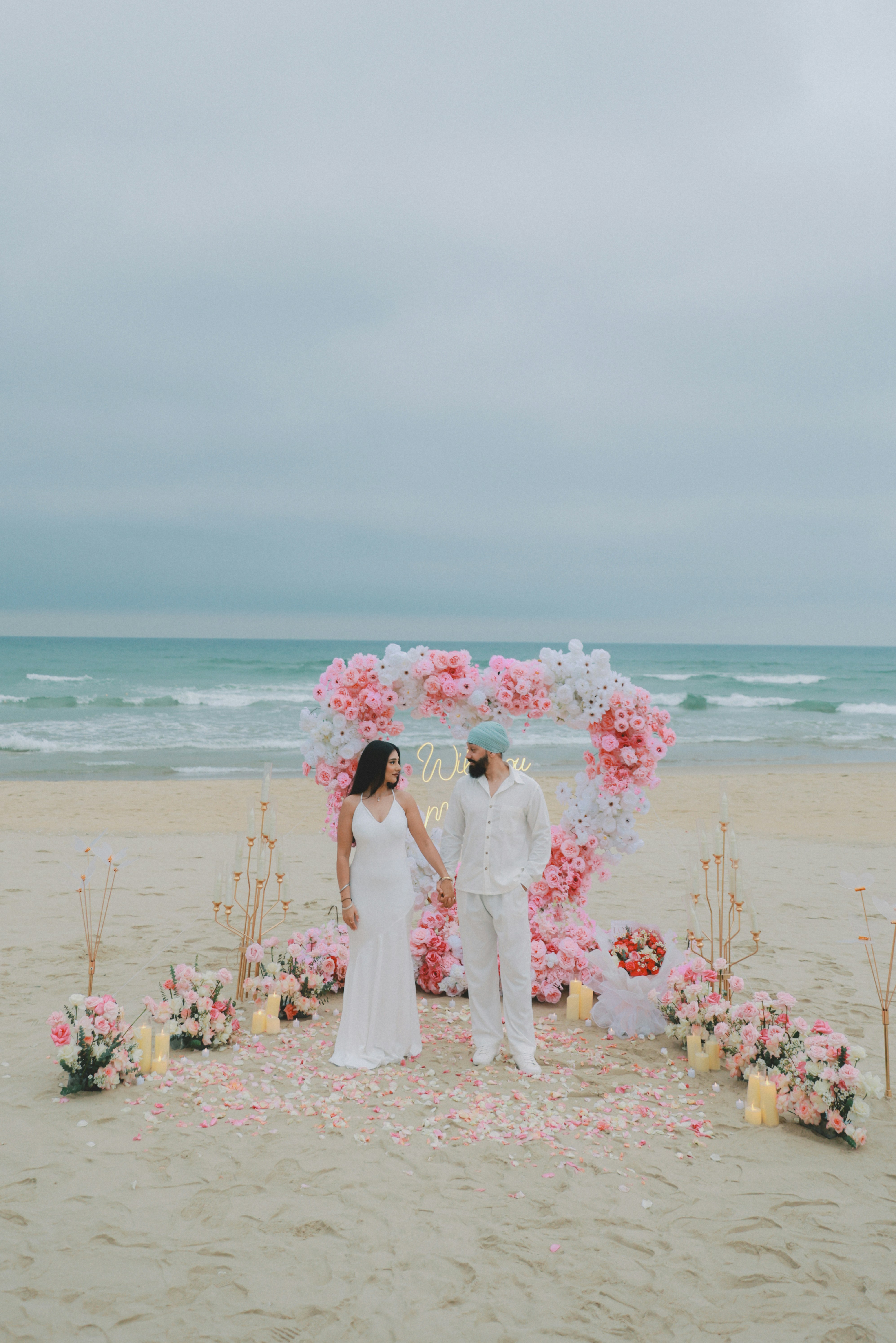 Ceremony under a blush arch: couple on the sunlit shoreline
