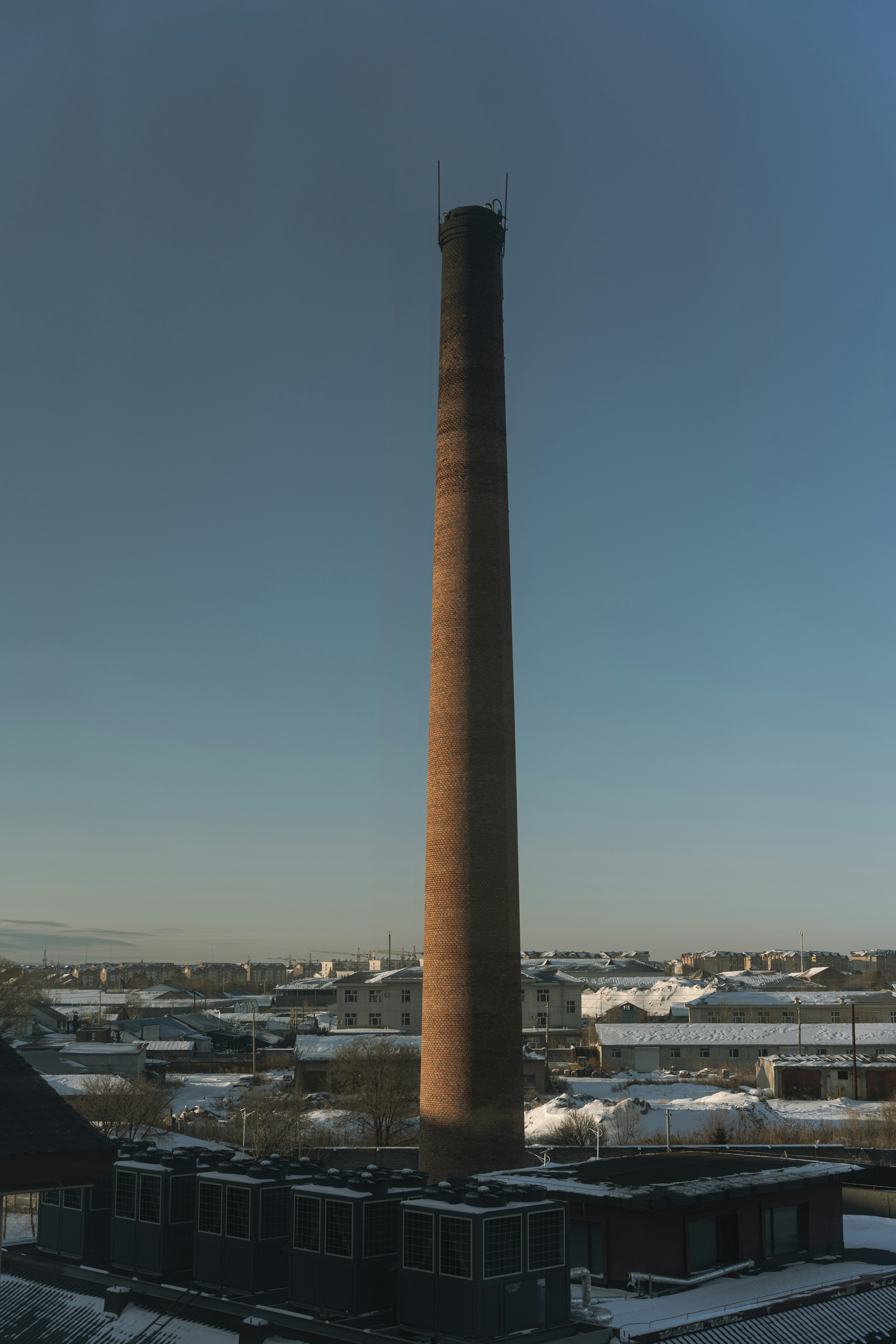 Industrial Sentinel: A Tall Brick Chimney Pierces a Snowlit Dawn