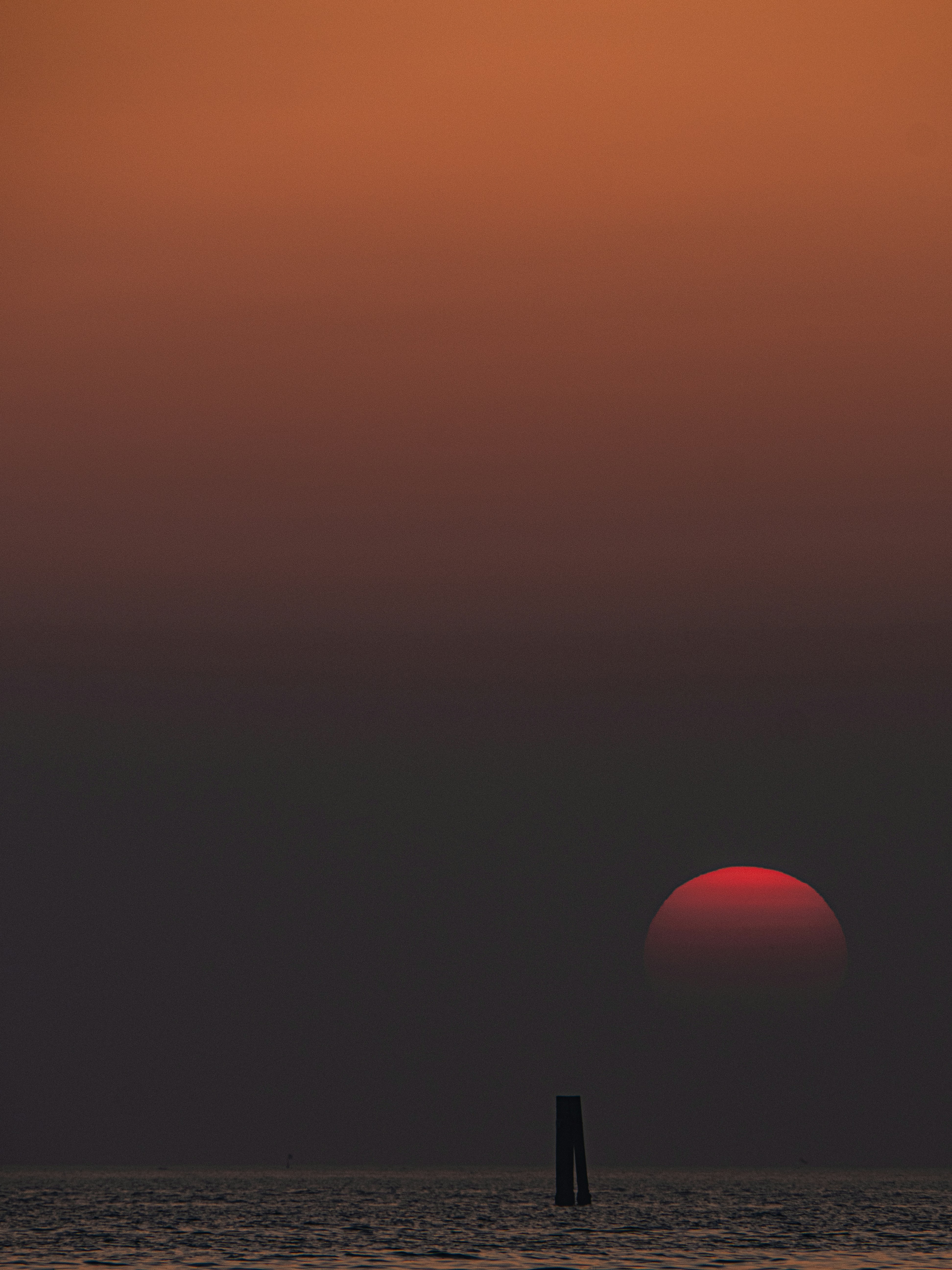 A large red sun setting over the ocean.