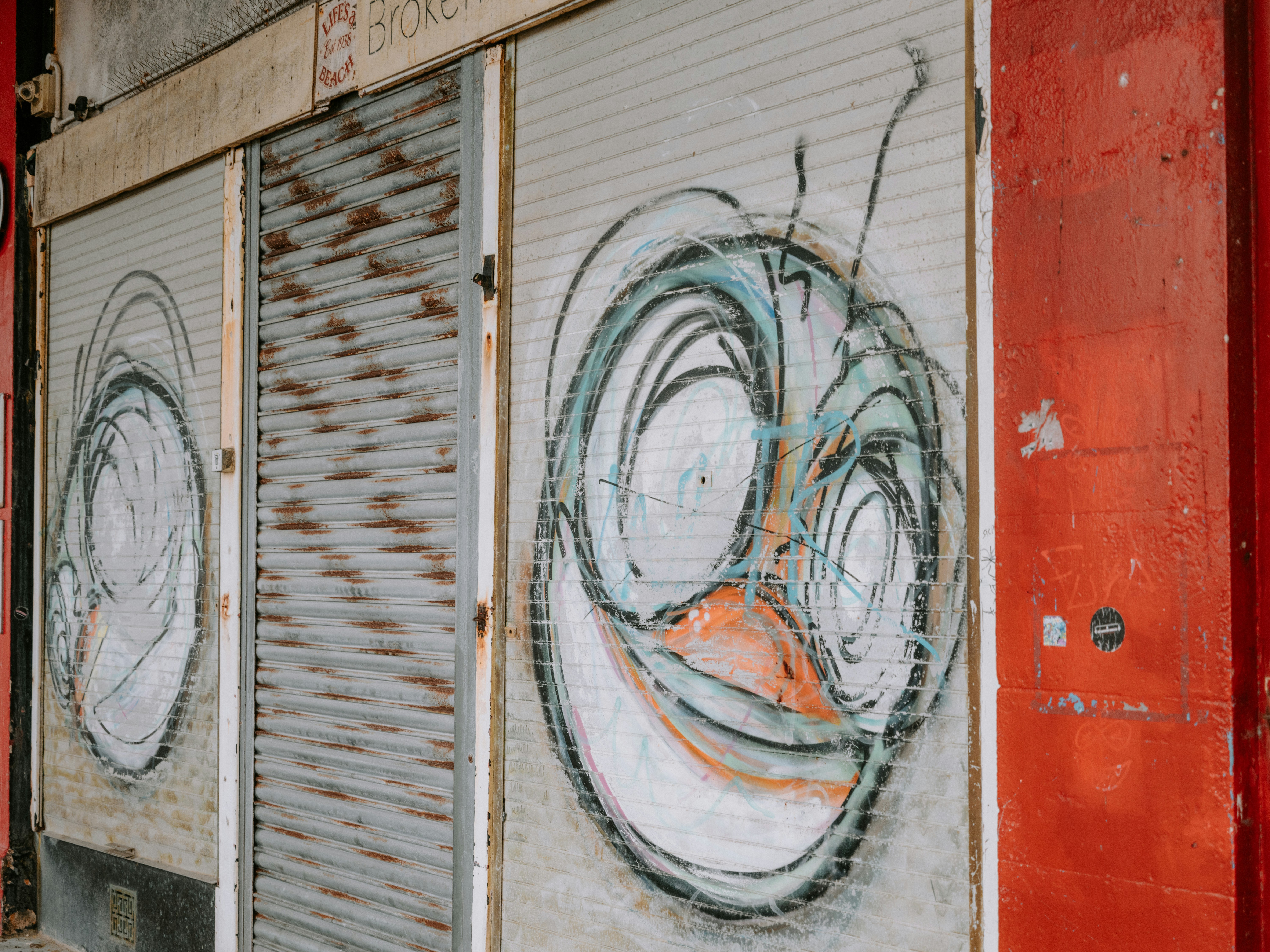 Graffiti Lens: A Cheery Eye in a Row of Closed Shutters