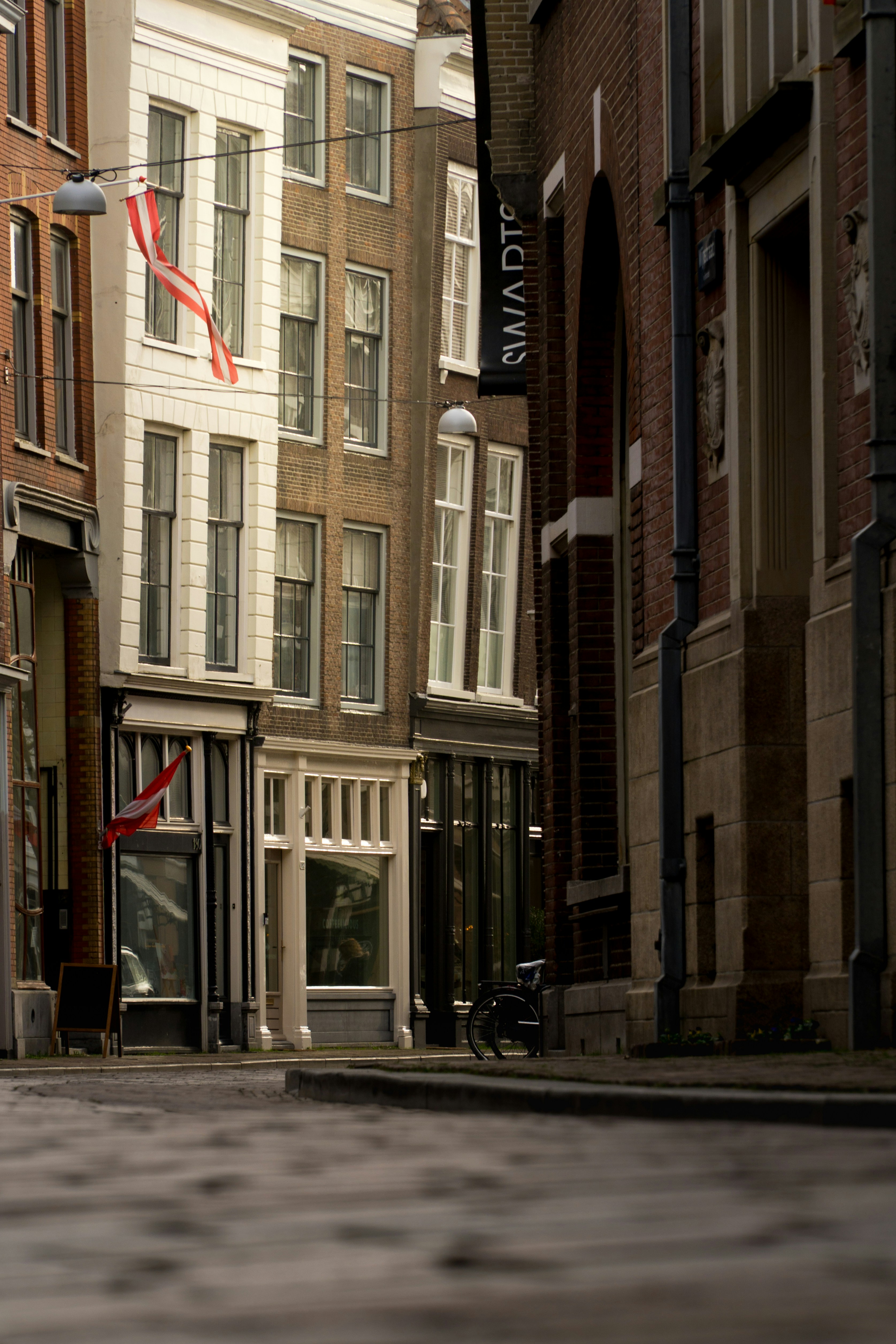 Narrow street with tall buildings and cobblestone pavement.