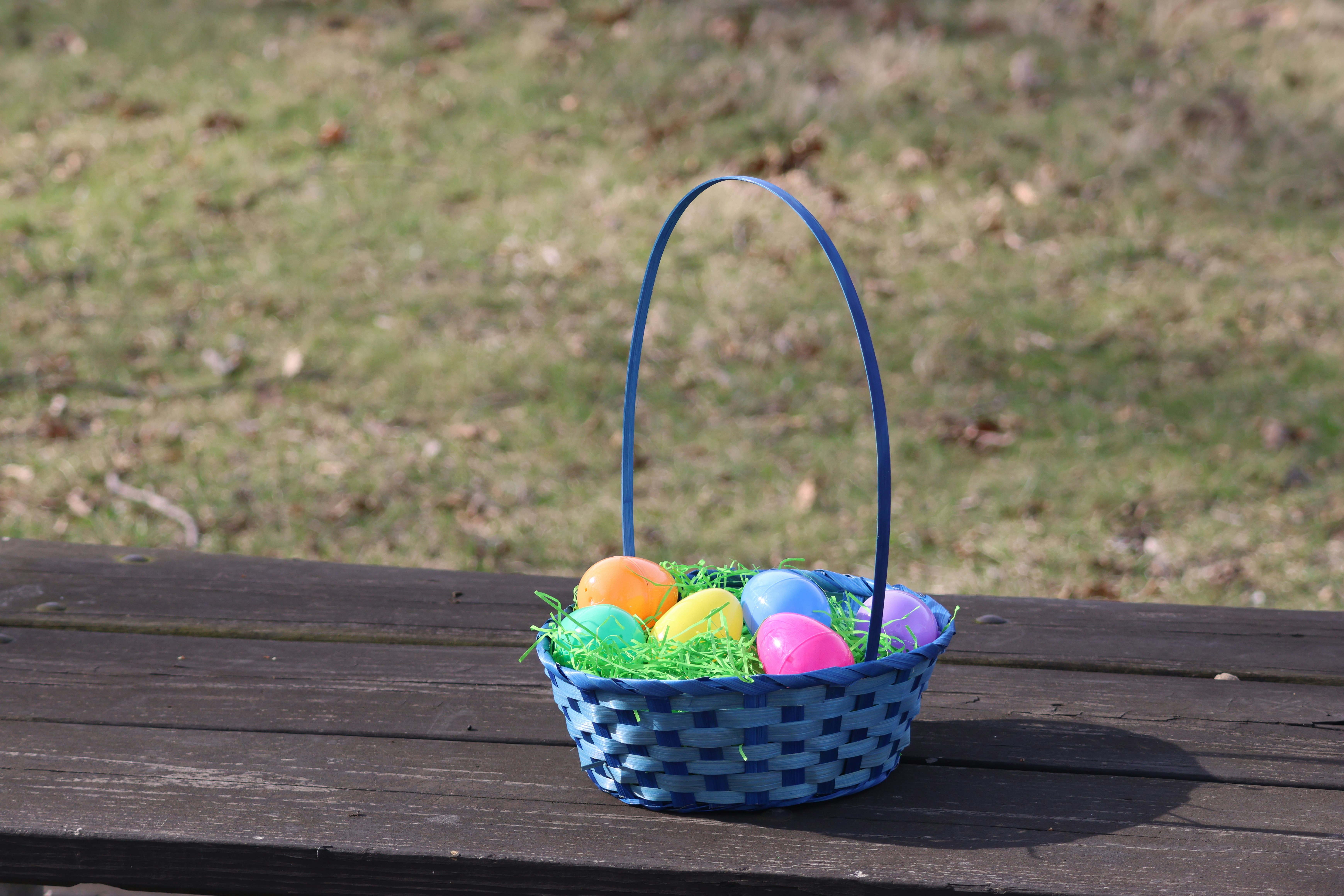 Blue woven basket of colorful Easter eggs resting on a wooden bench