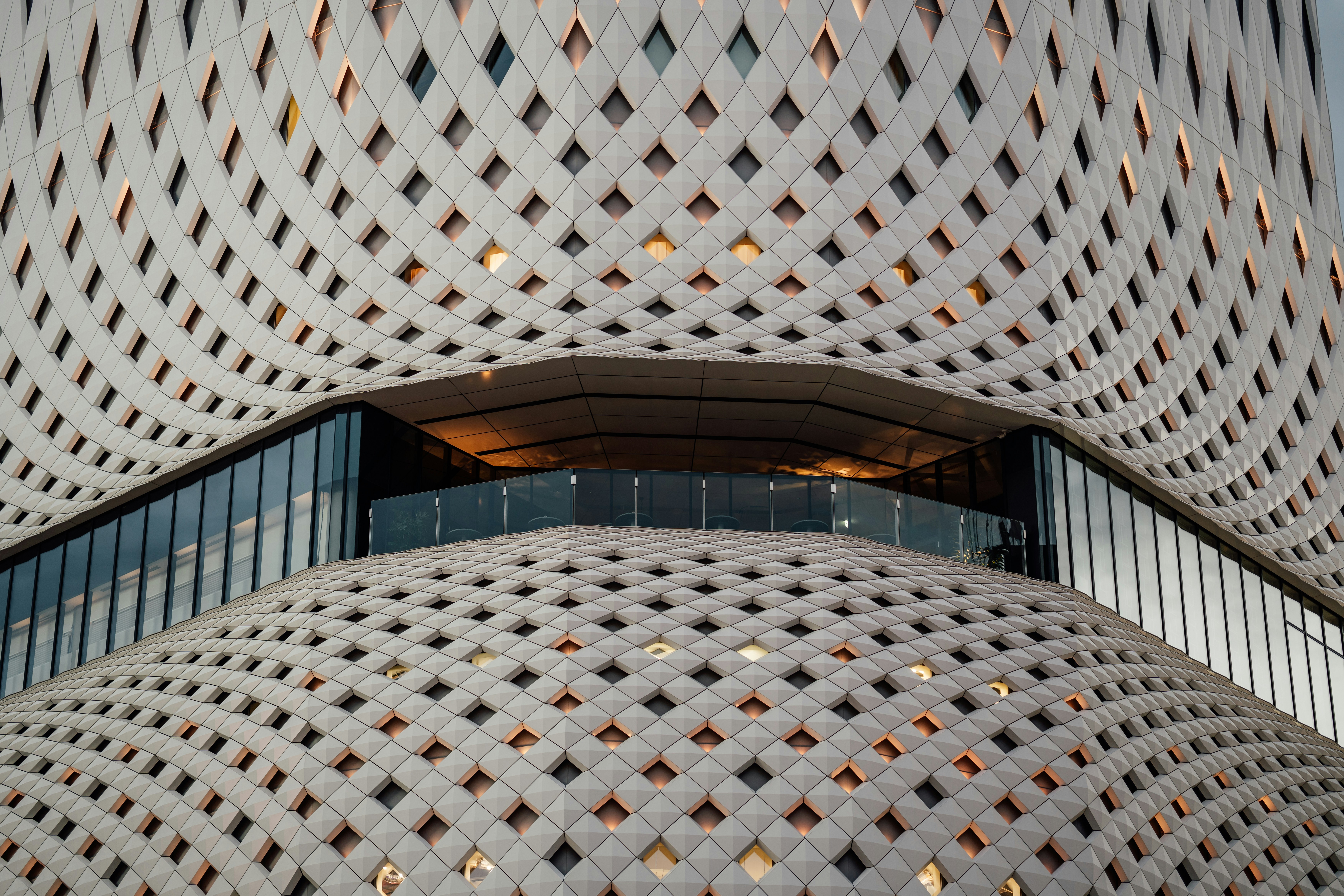 Curved Facade of a Diamond Mesh Building Framing a Glass Balcony