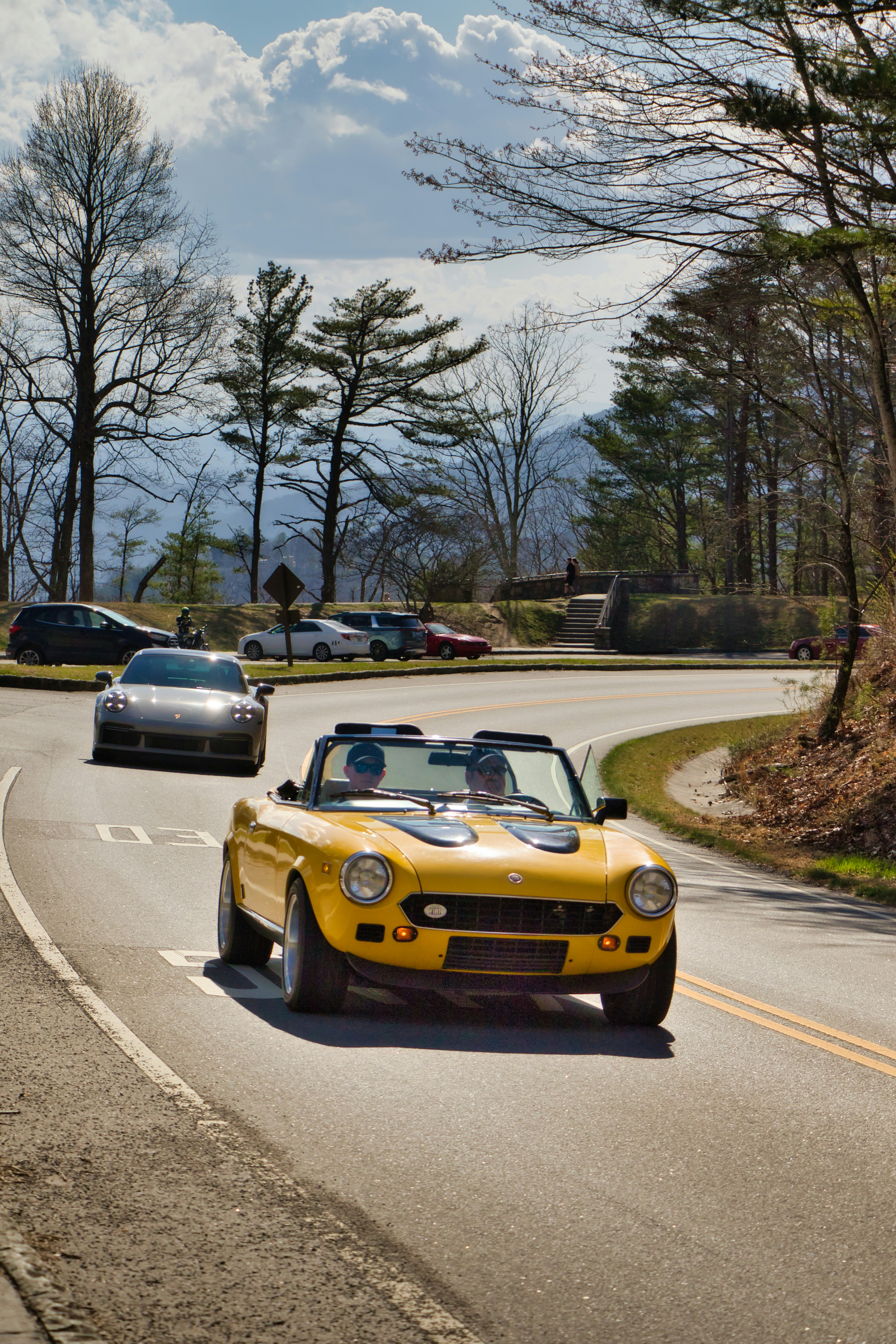 Yellow Convertible Cresting a Winding Road with Mountain Backdrop