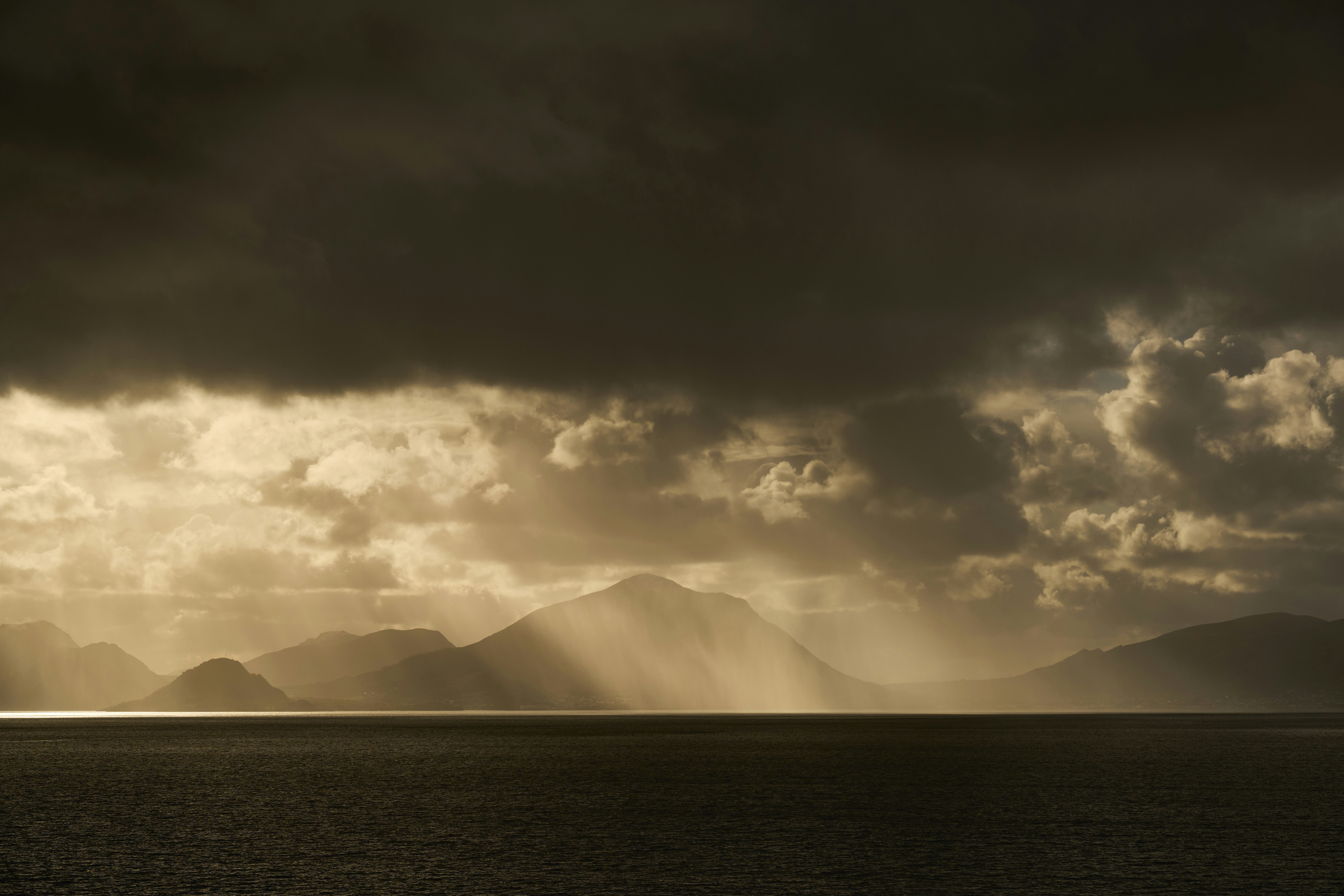 Sunlight streams through stormy clouds over distant mountains.