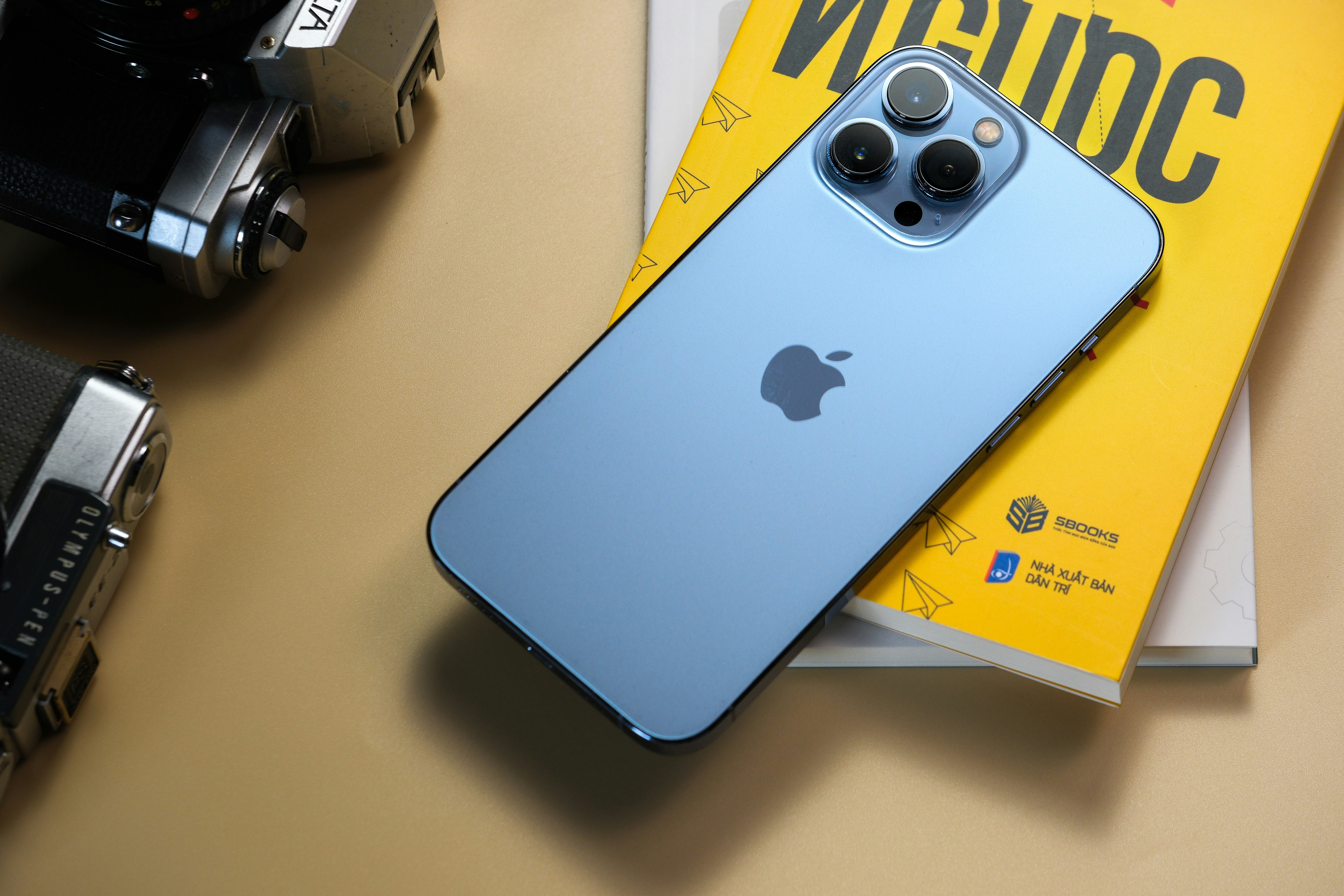 Blue iPhone 14 Pro lying atop a yellow magazine with vintage cameras in the background