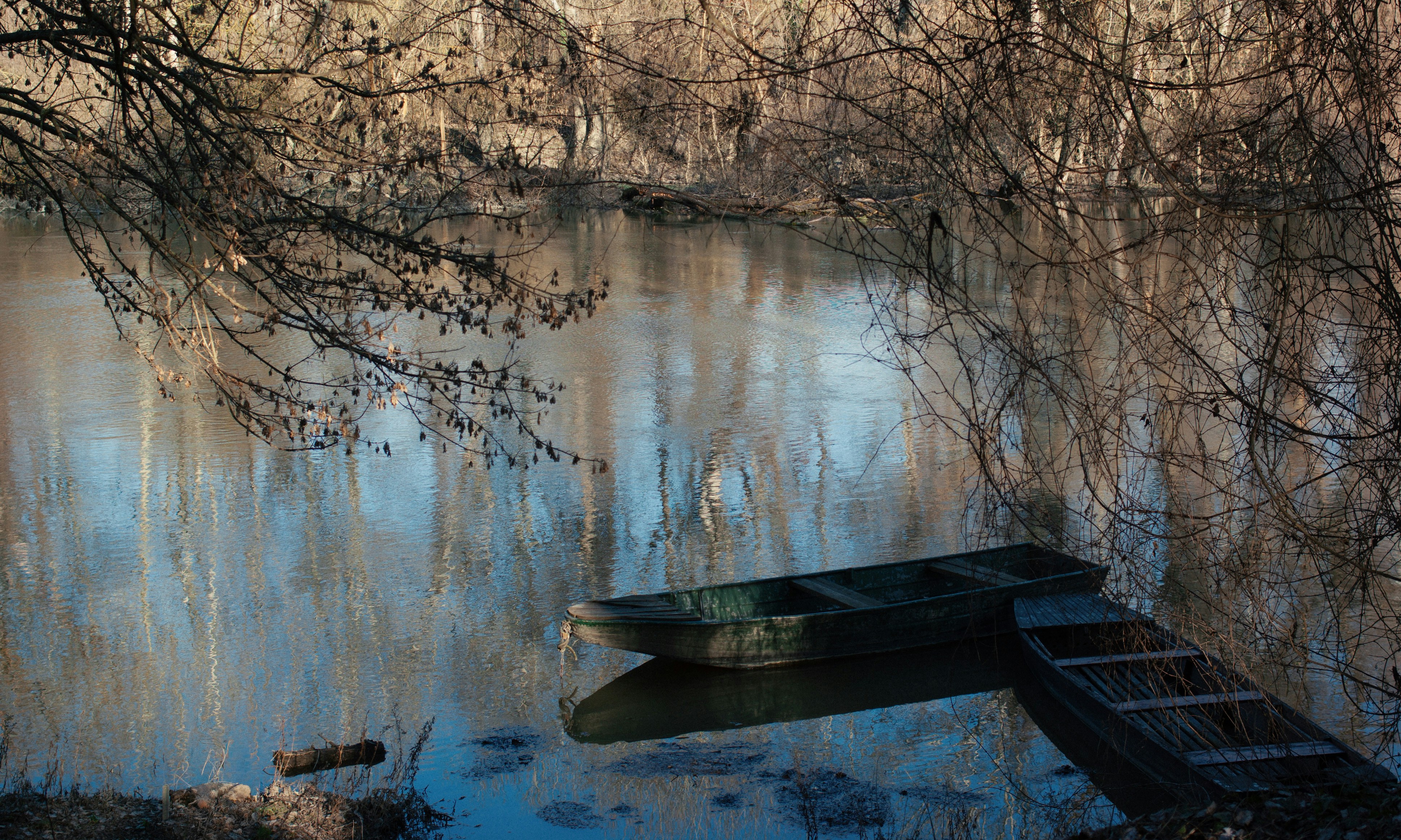 Two old boats rest on a calm river.