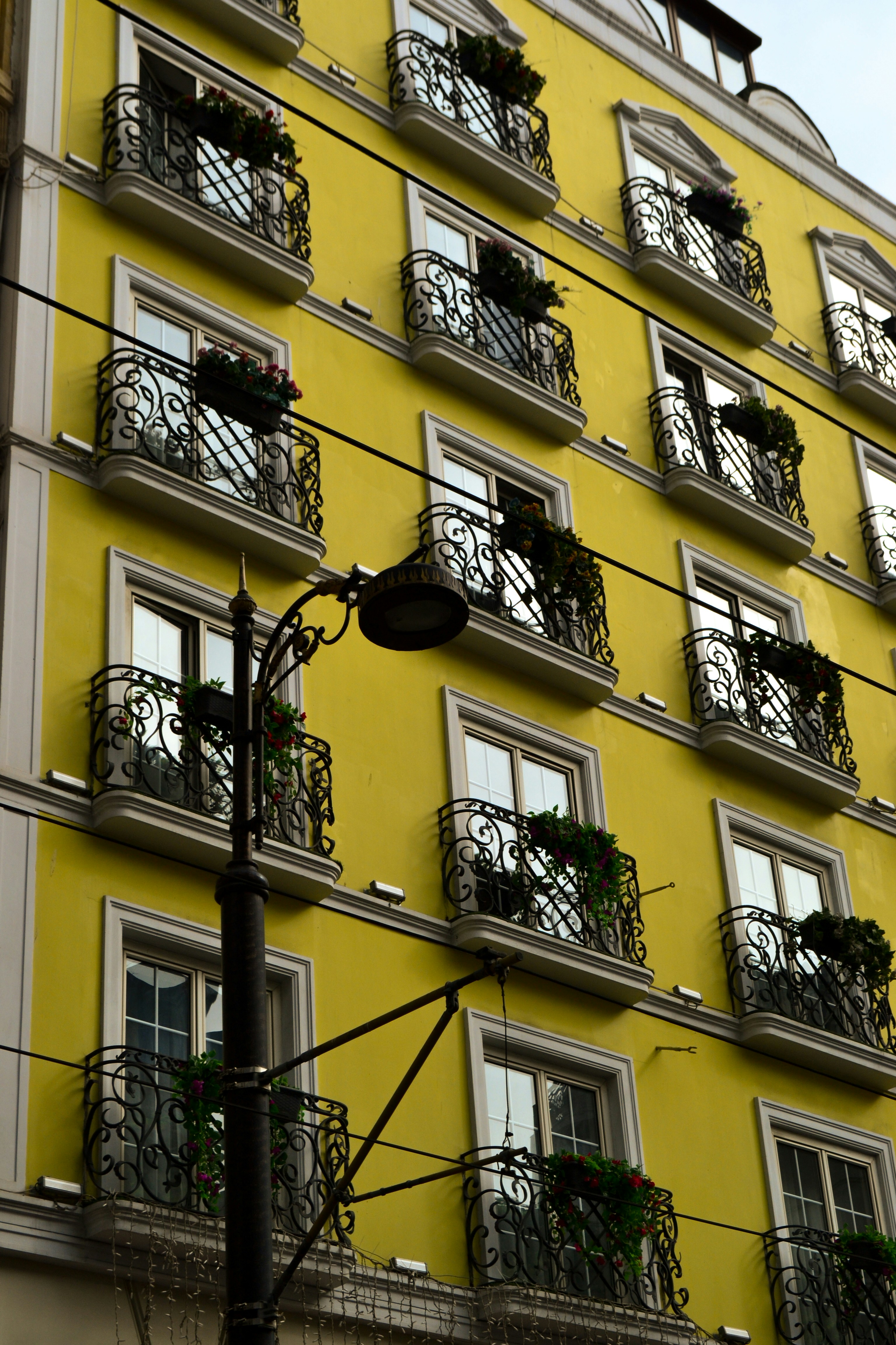 Yellow townhouse with wrought-iron balconies under a streetlamp