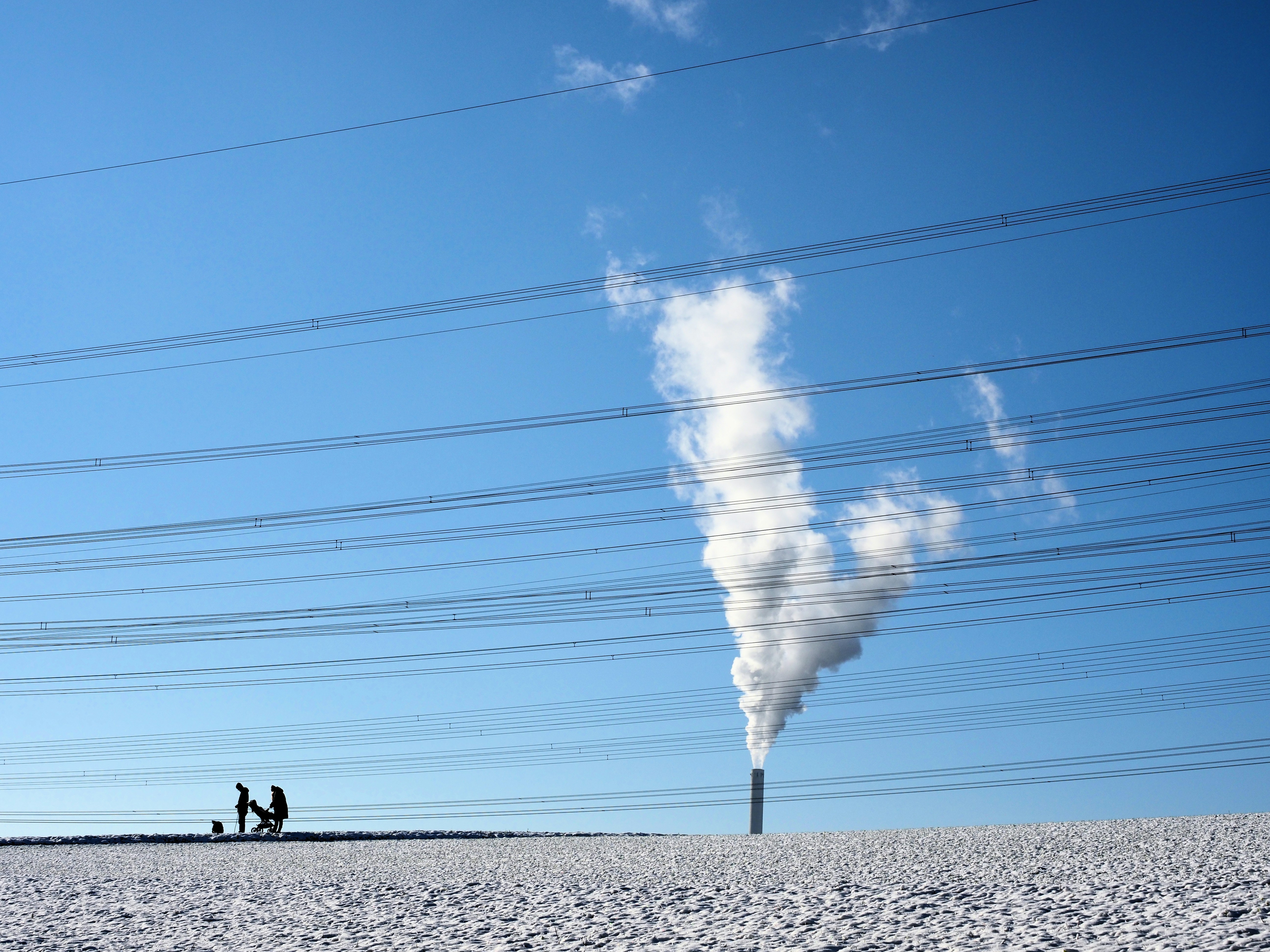 Two silhouettes and a smokestack: horizon line of industry under a clear blue sky