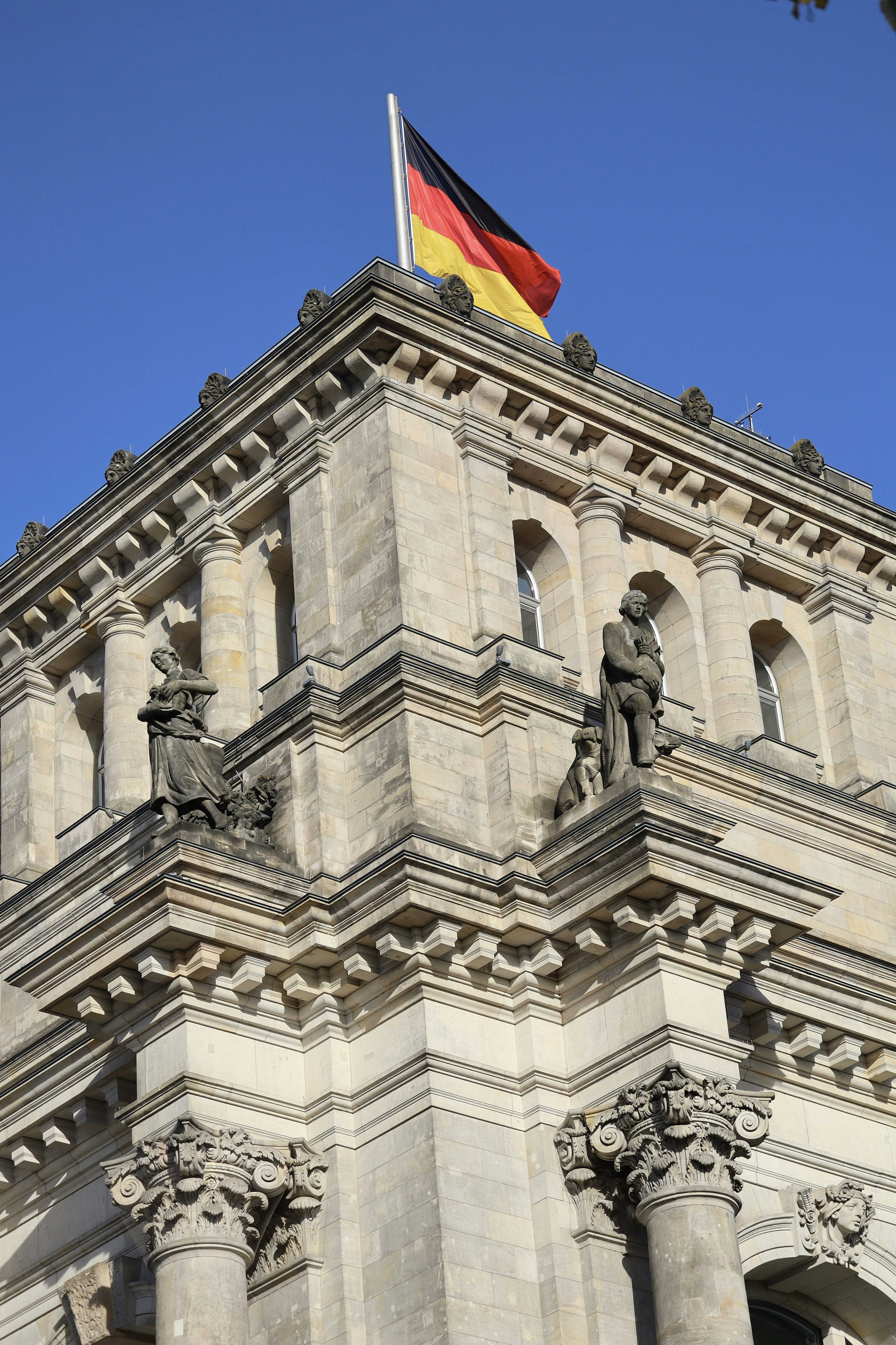 Flag atop a historic Berlin facade crowned with statues