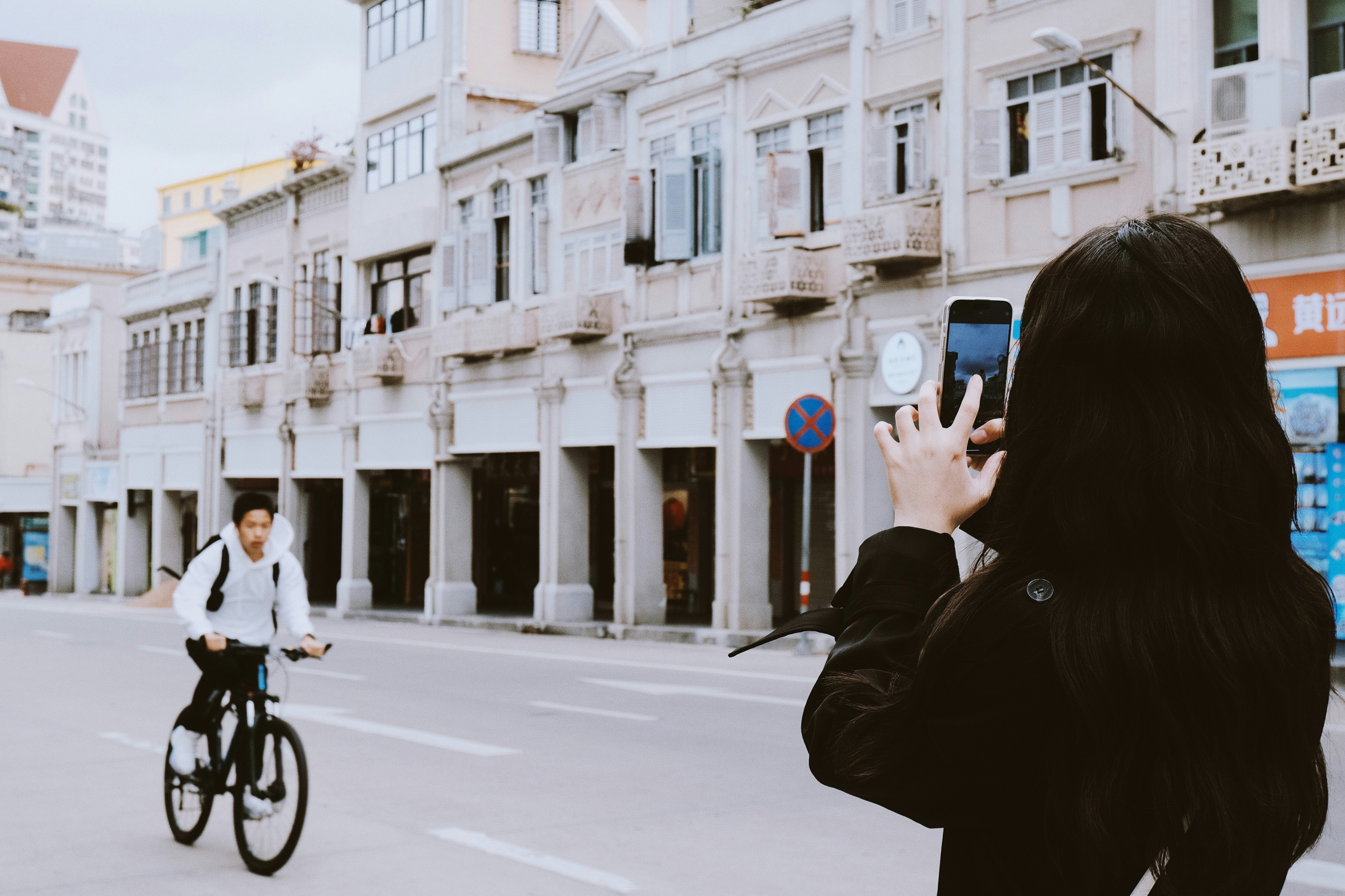 A candid street capture: a woman in the foreground frames a cyclist in motion