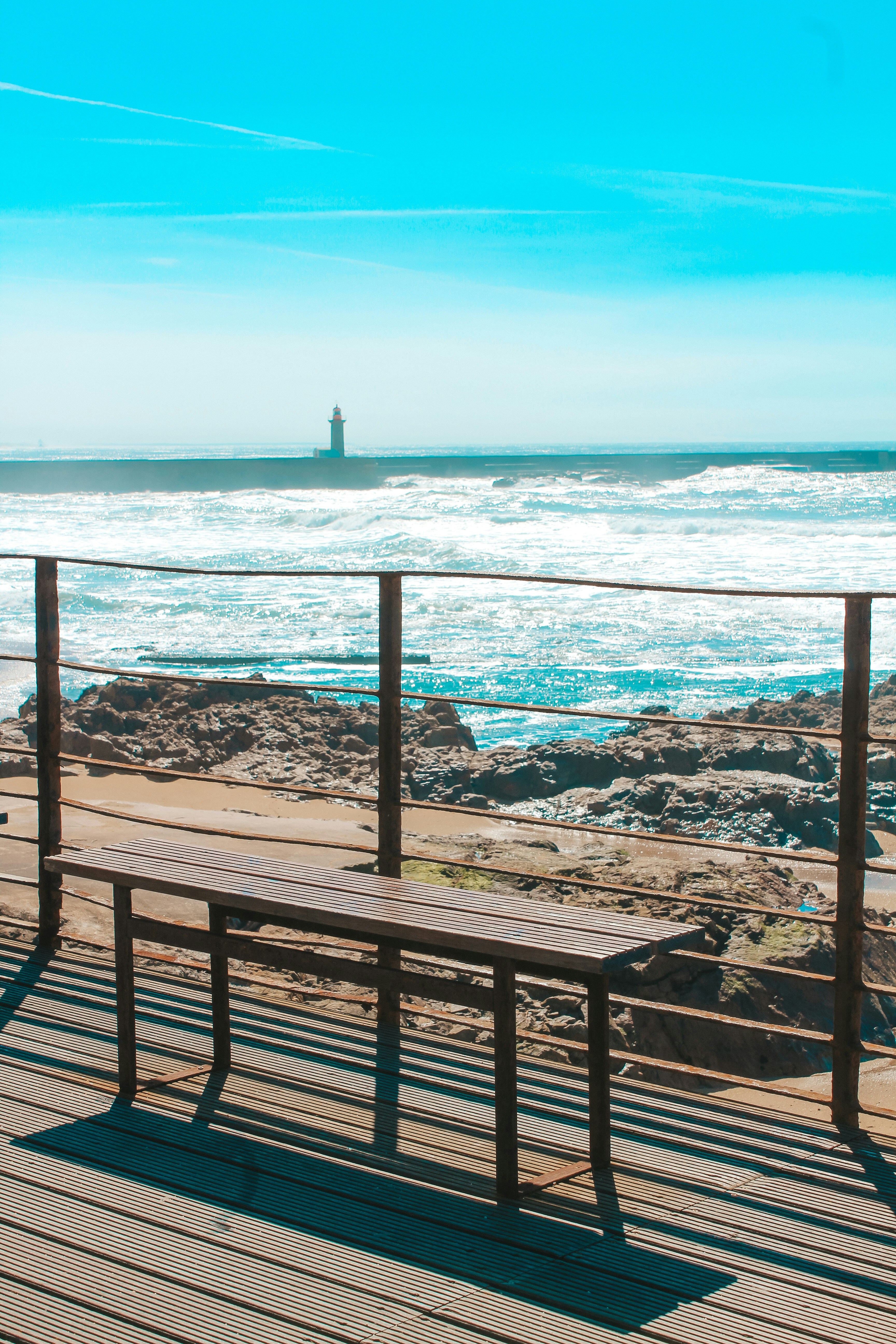 Toward the Horizon: bench and railing frame a sunlit seascape with lighthouse