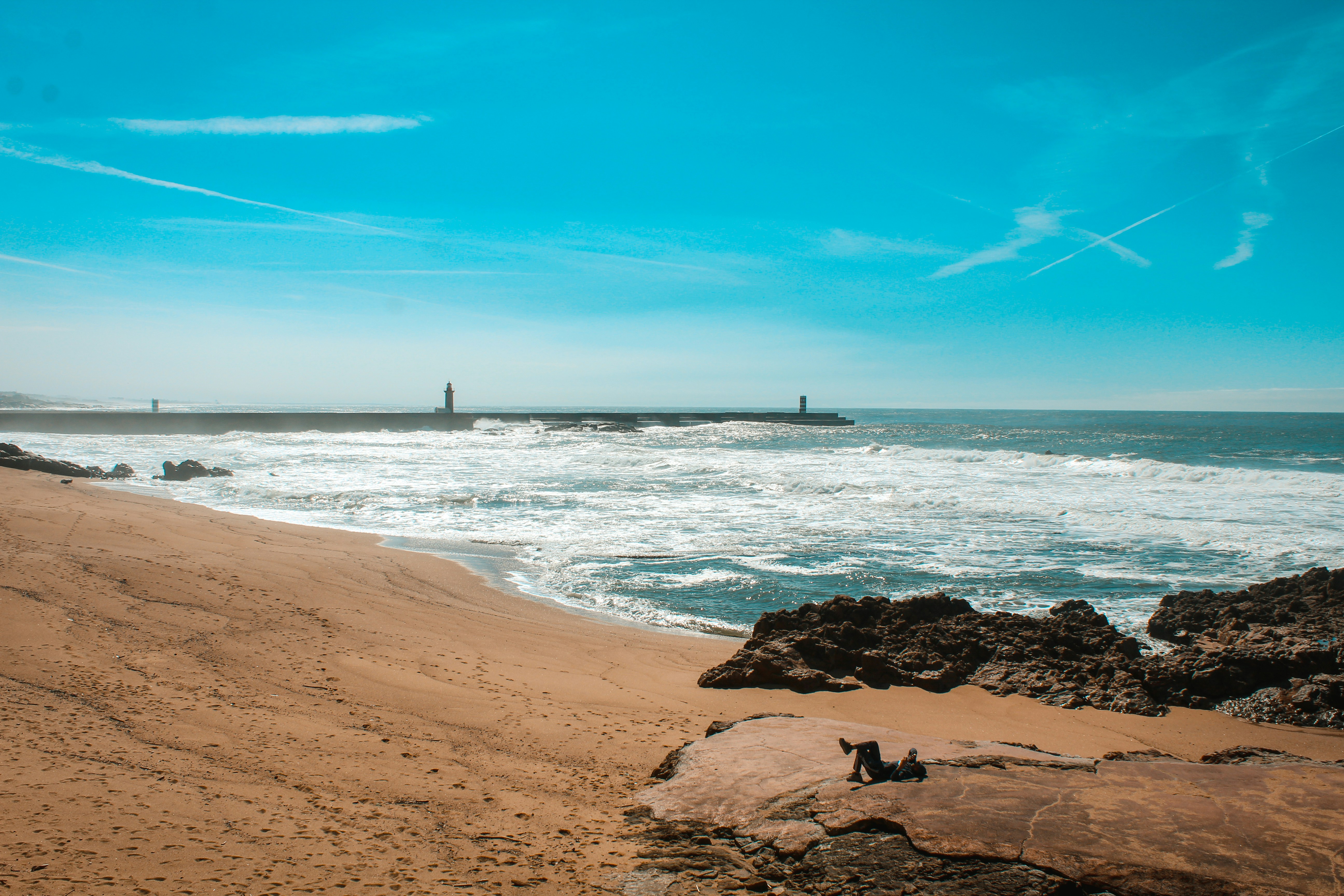 Coastal Quiet: Sunlit Sand, Sea Sillouette, and Distant Breakwater