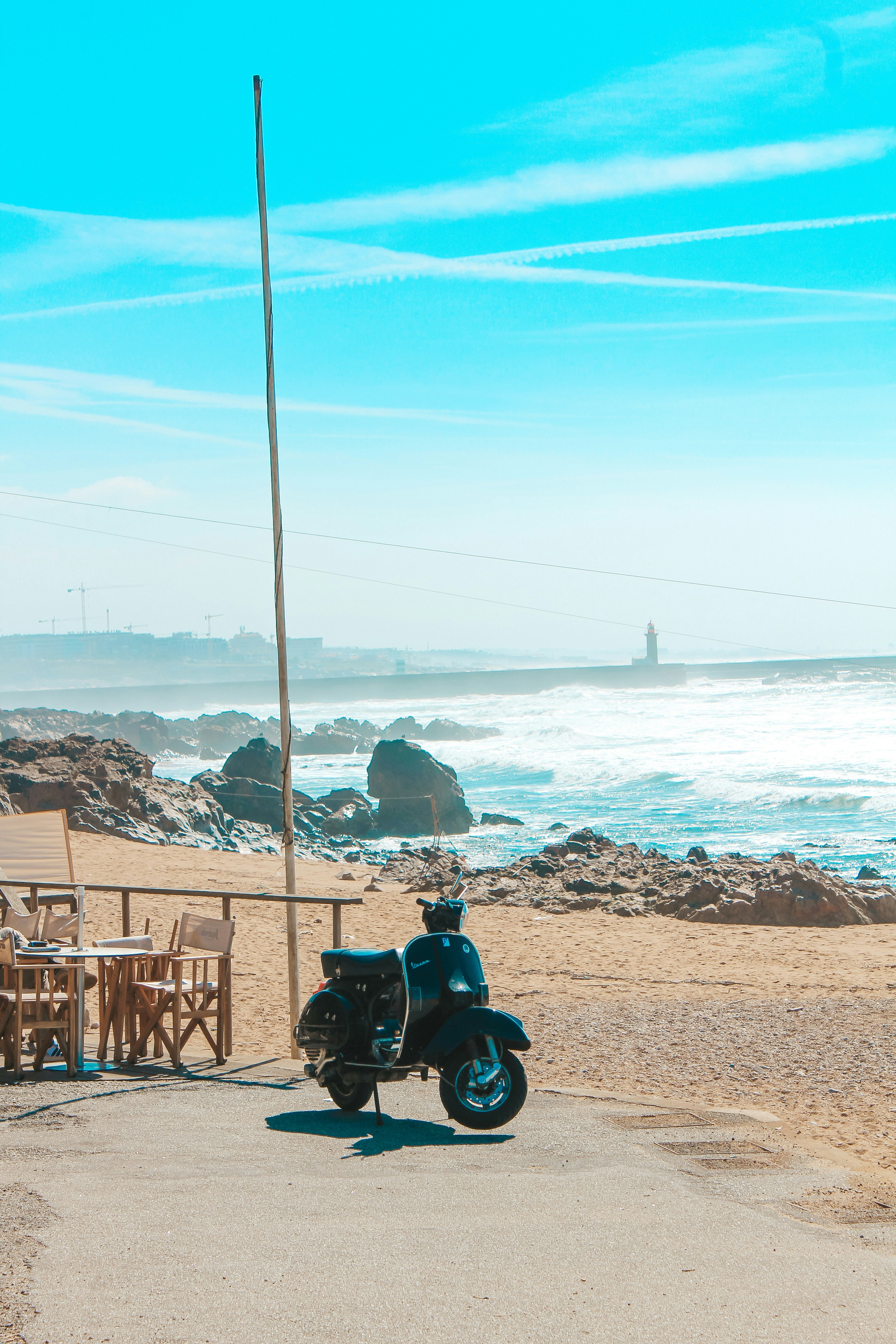 Blue Scooter on a Sunny Beach with Seaside Rocks and Lighthouse