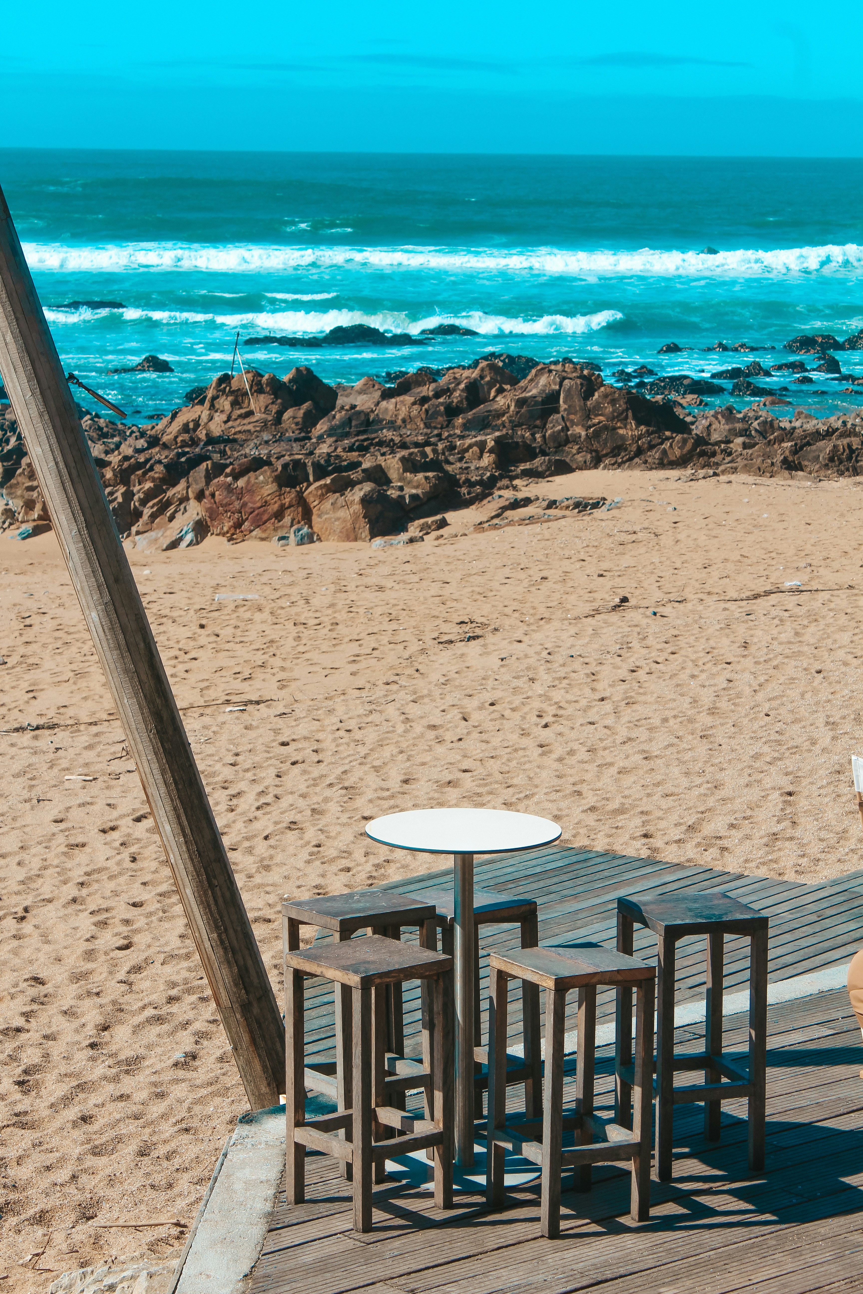 Seaside Terrace: Weathered Tables on a Sandy Deck with Ocean Rocks