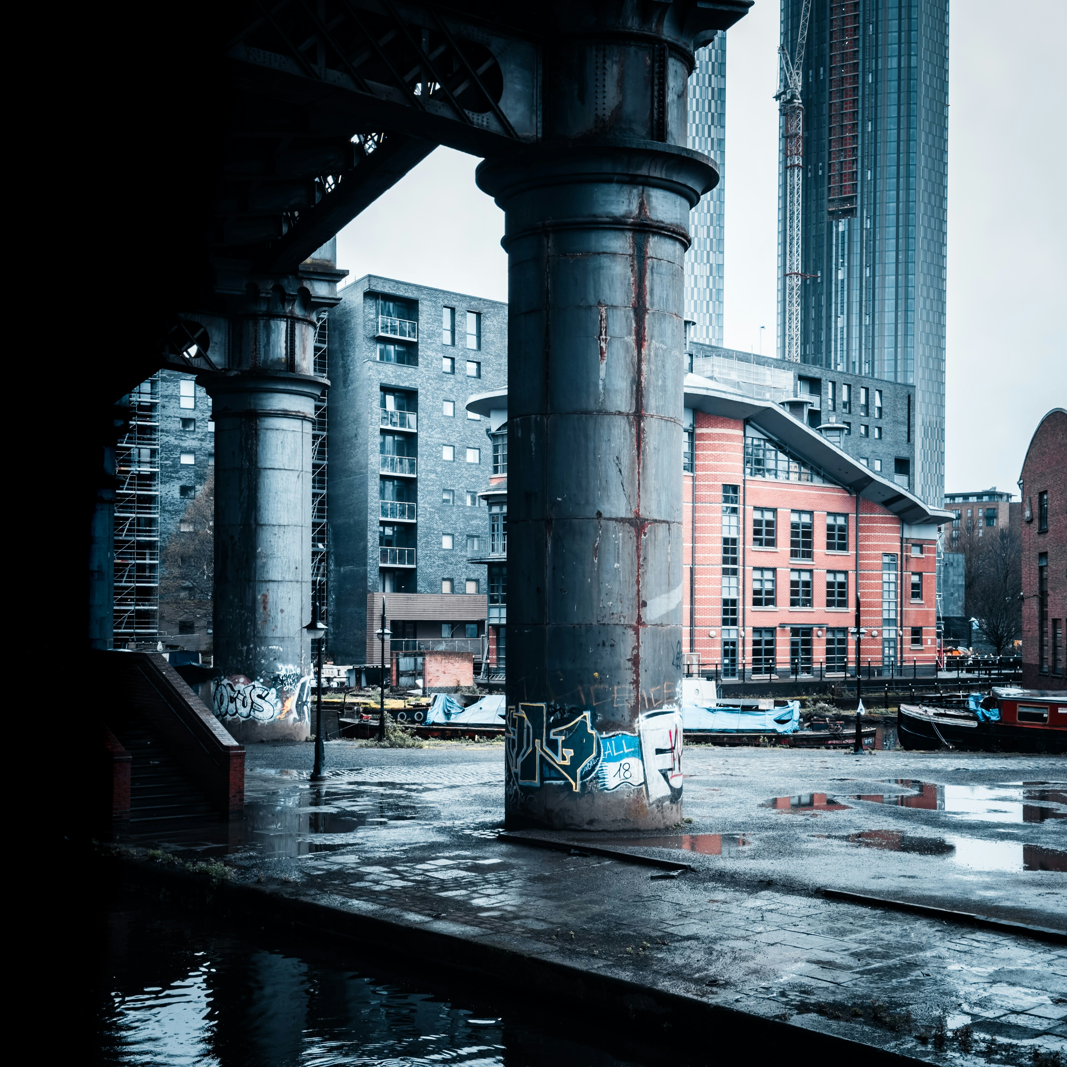 Under the Industrial Arch: Wet Courtyard Beneath a Towering Pier