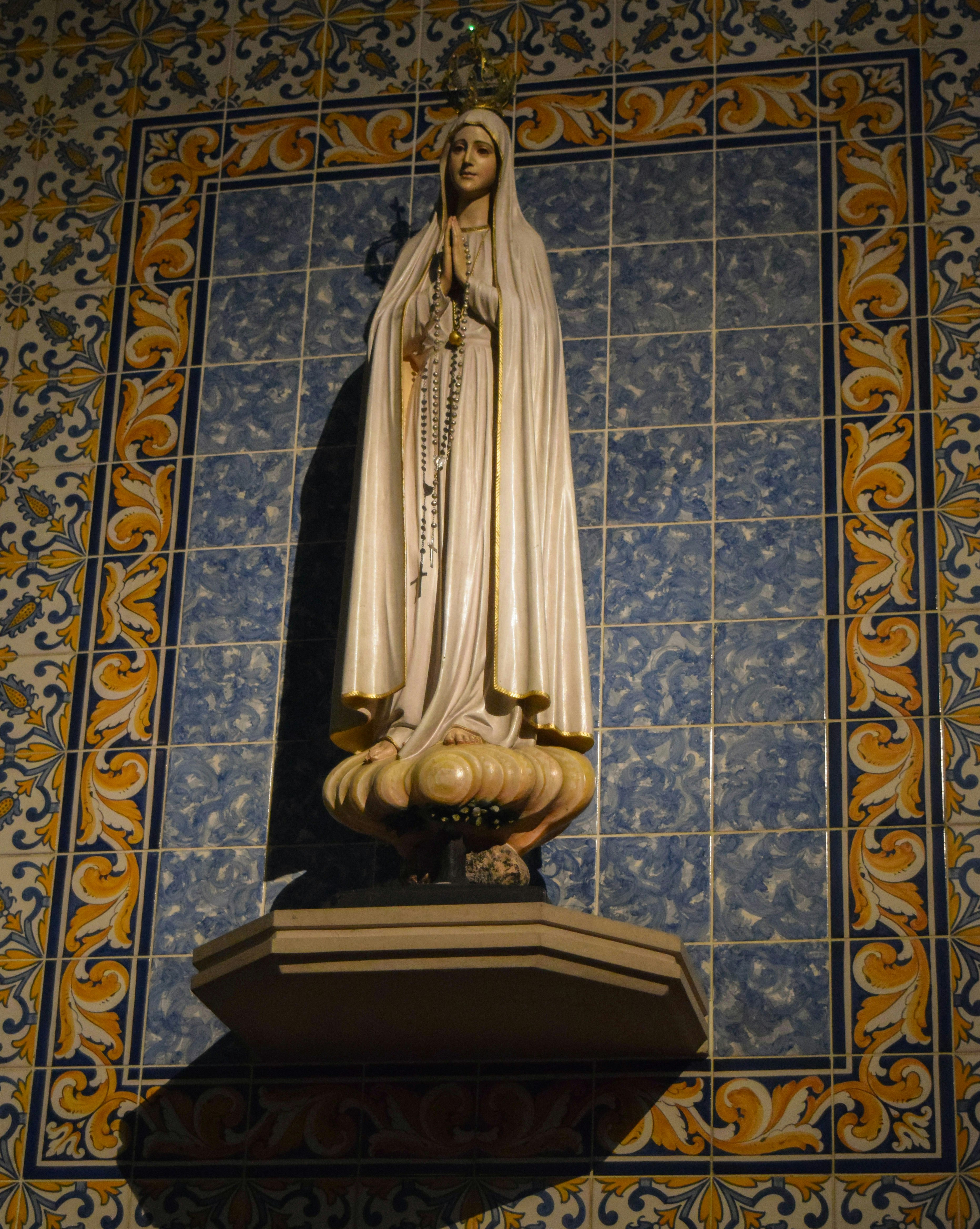 Quiet Reverence: The Virgin Statue Against Ornate Blue Tile Backdrop