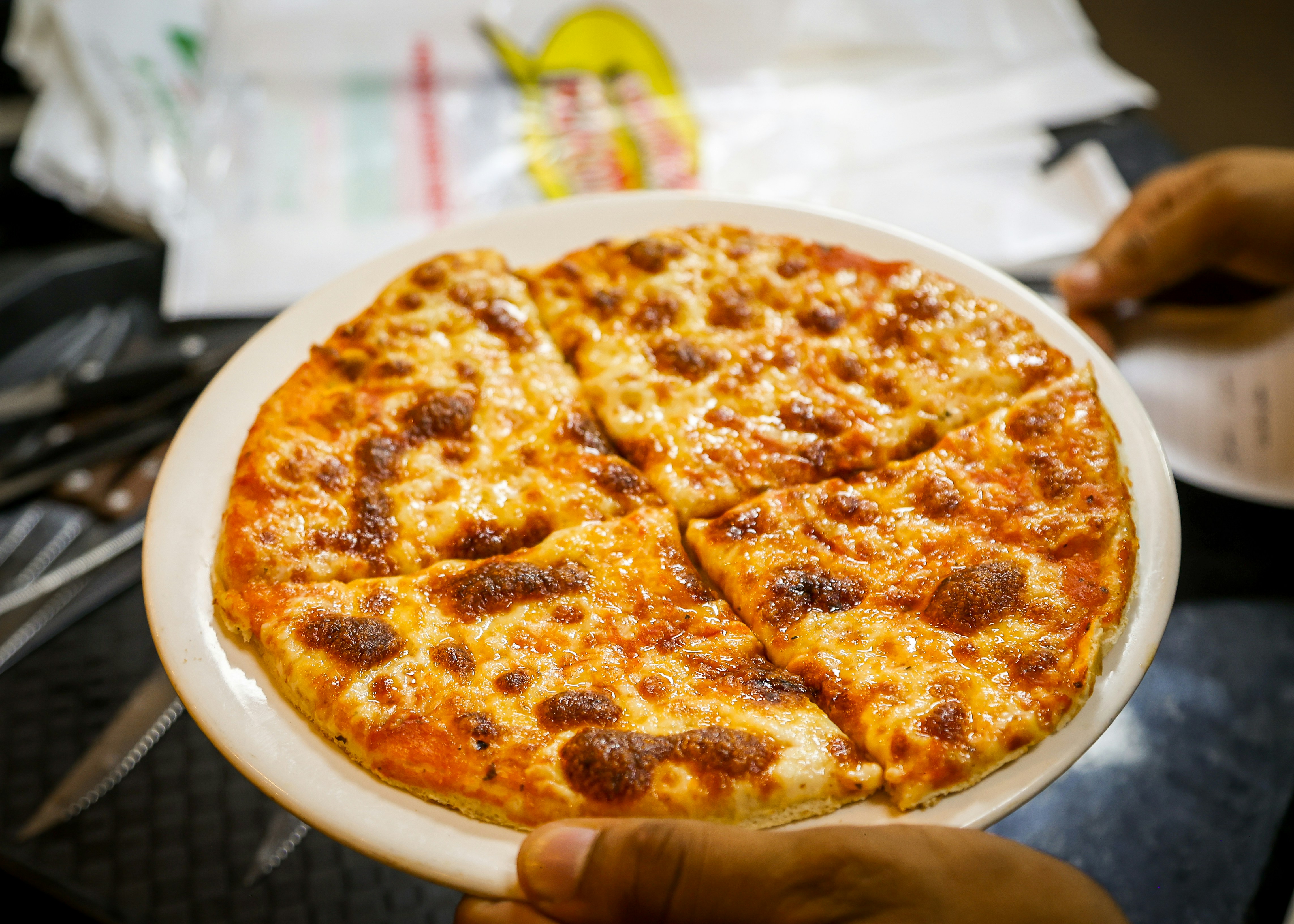 Hands stabilize a sizzling cheese pizza above a white plate