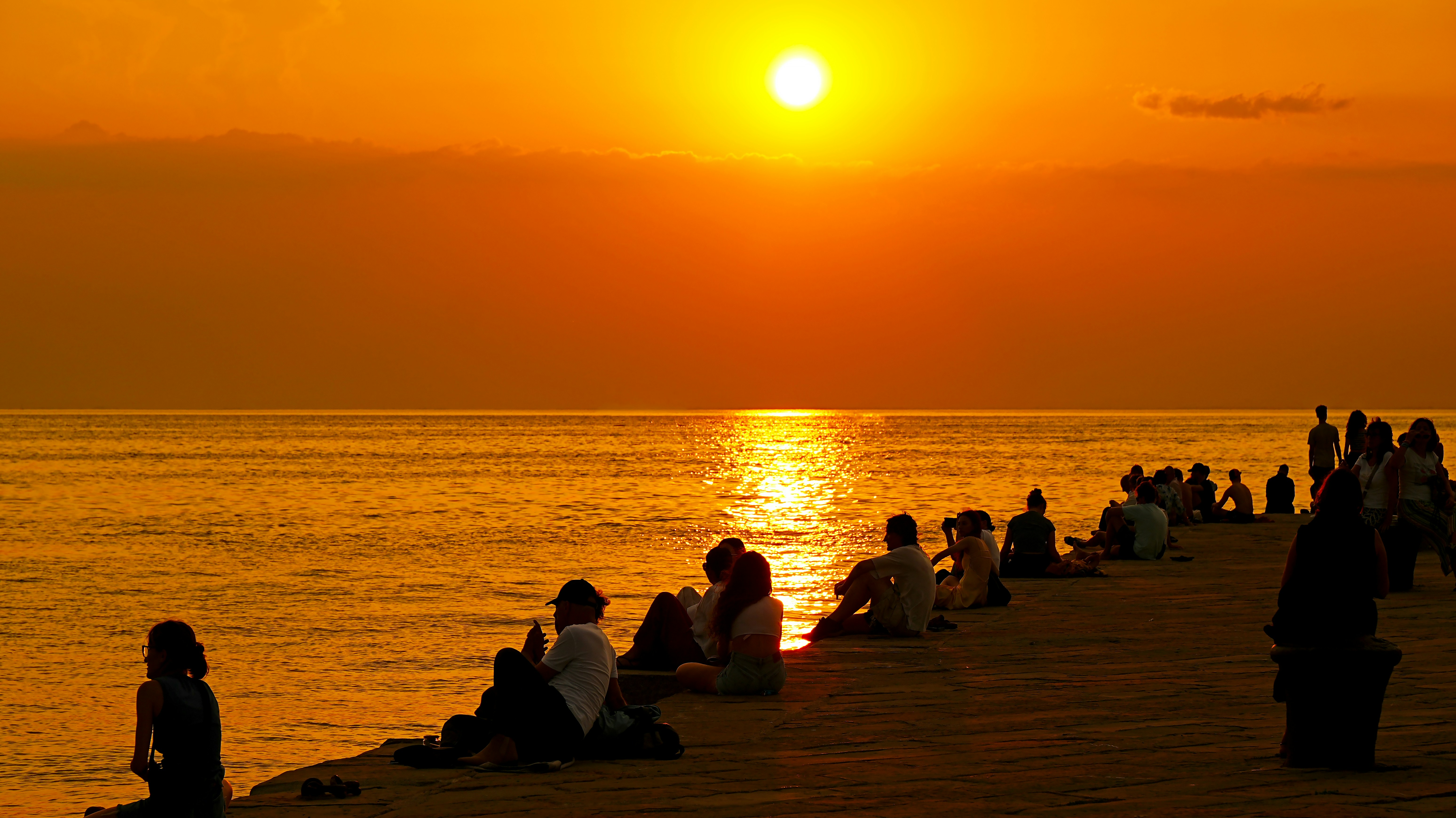 Sunset Assembly: People Gather Along the Pier as a Golden Sea Basks in Dusk