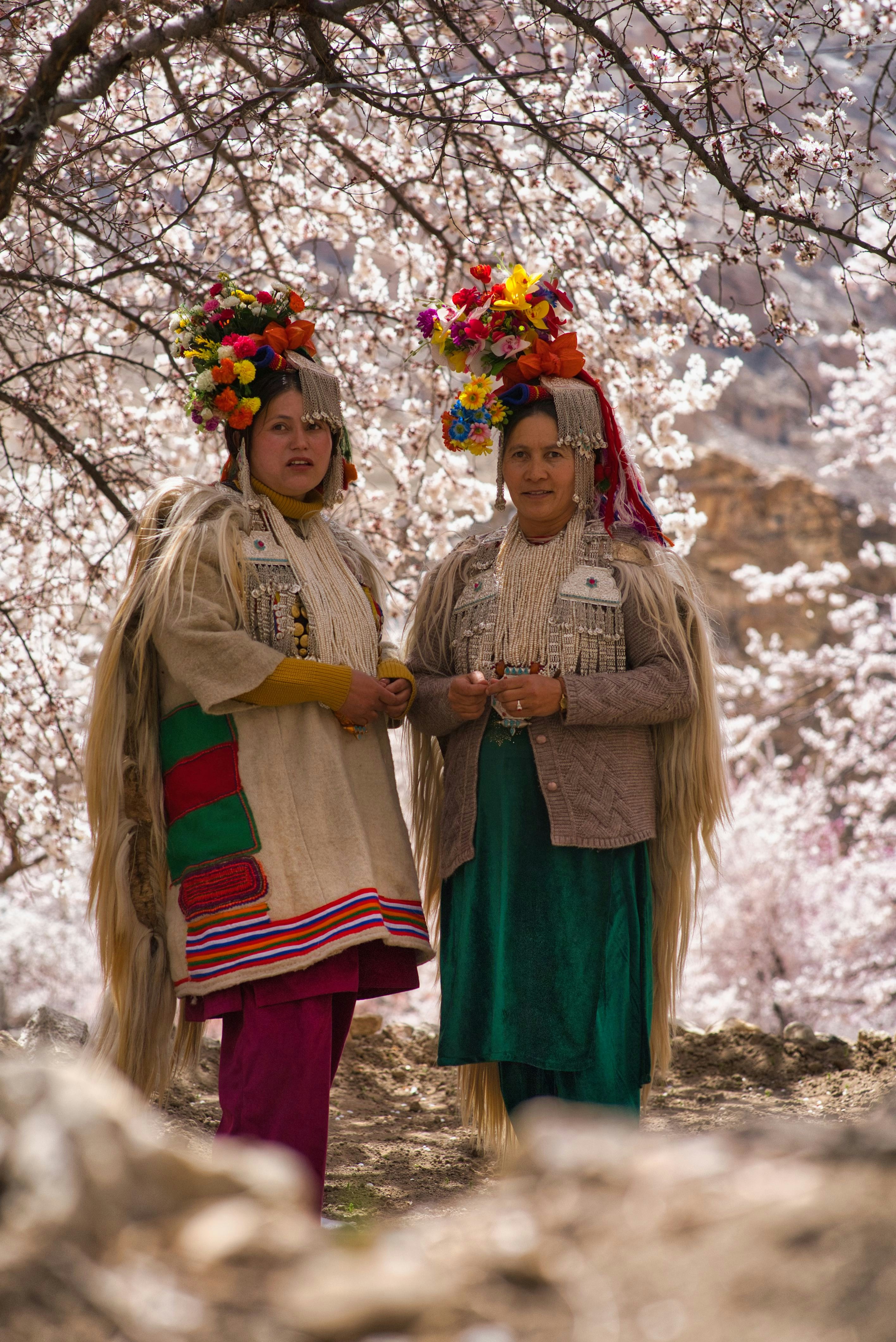 Two women in traditional attire stand under blooming trees