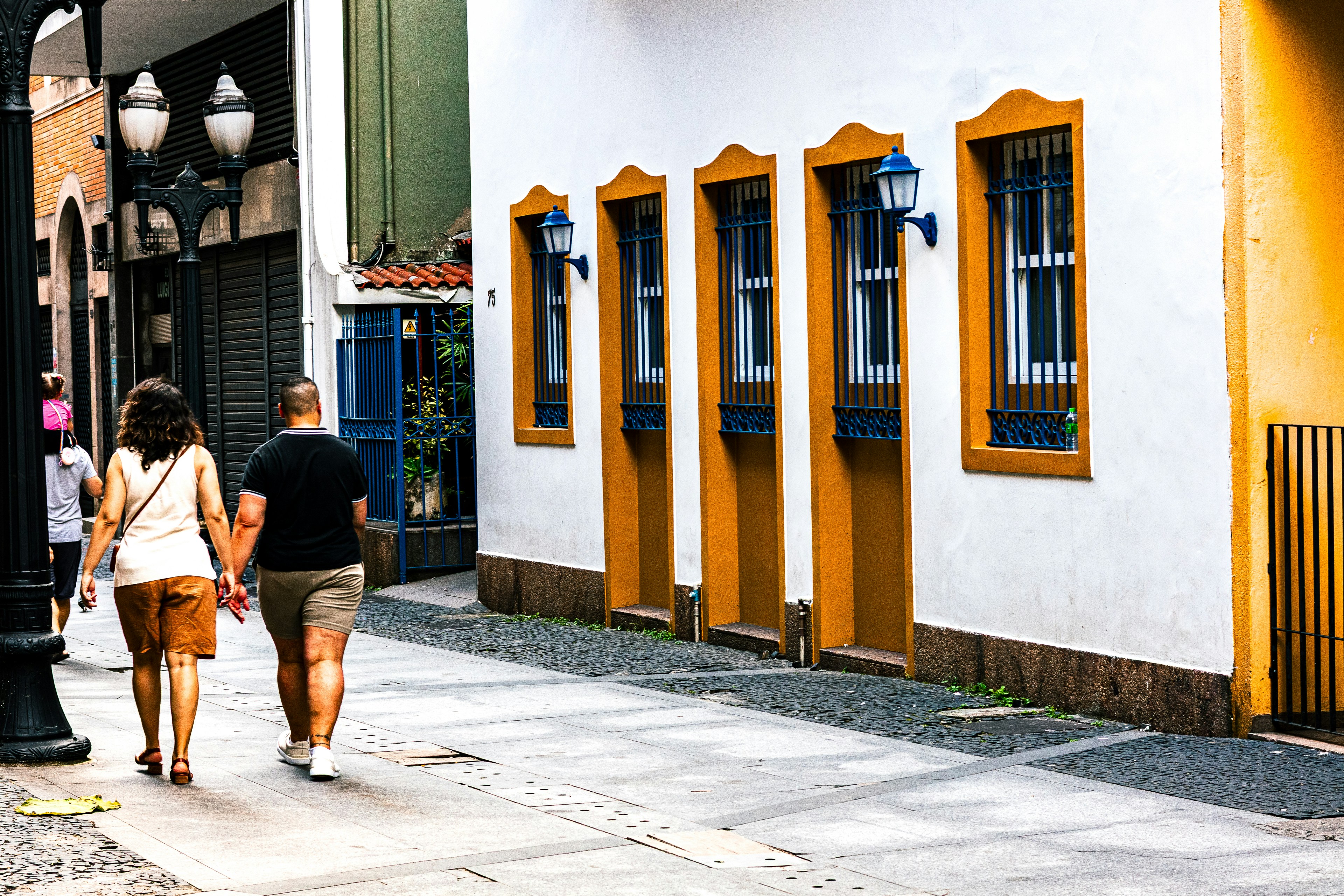 Two walkers in a sunlit Calle: Colourful colonial facades and a quiet stroll