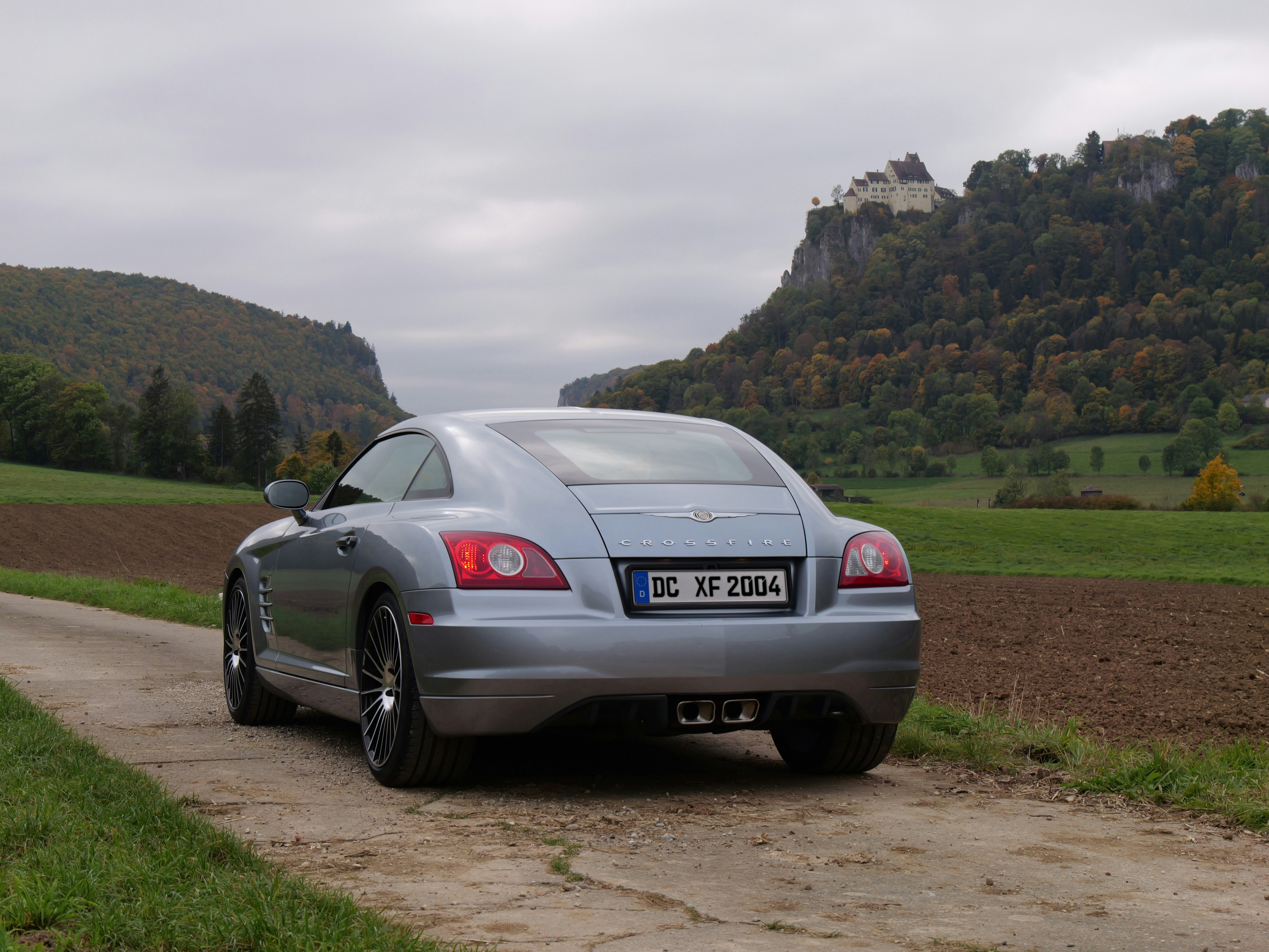 Silver Coupe on a Rural Road with a Castle Hillbackdrop