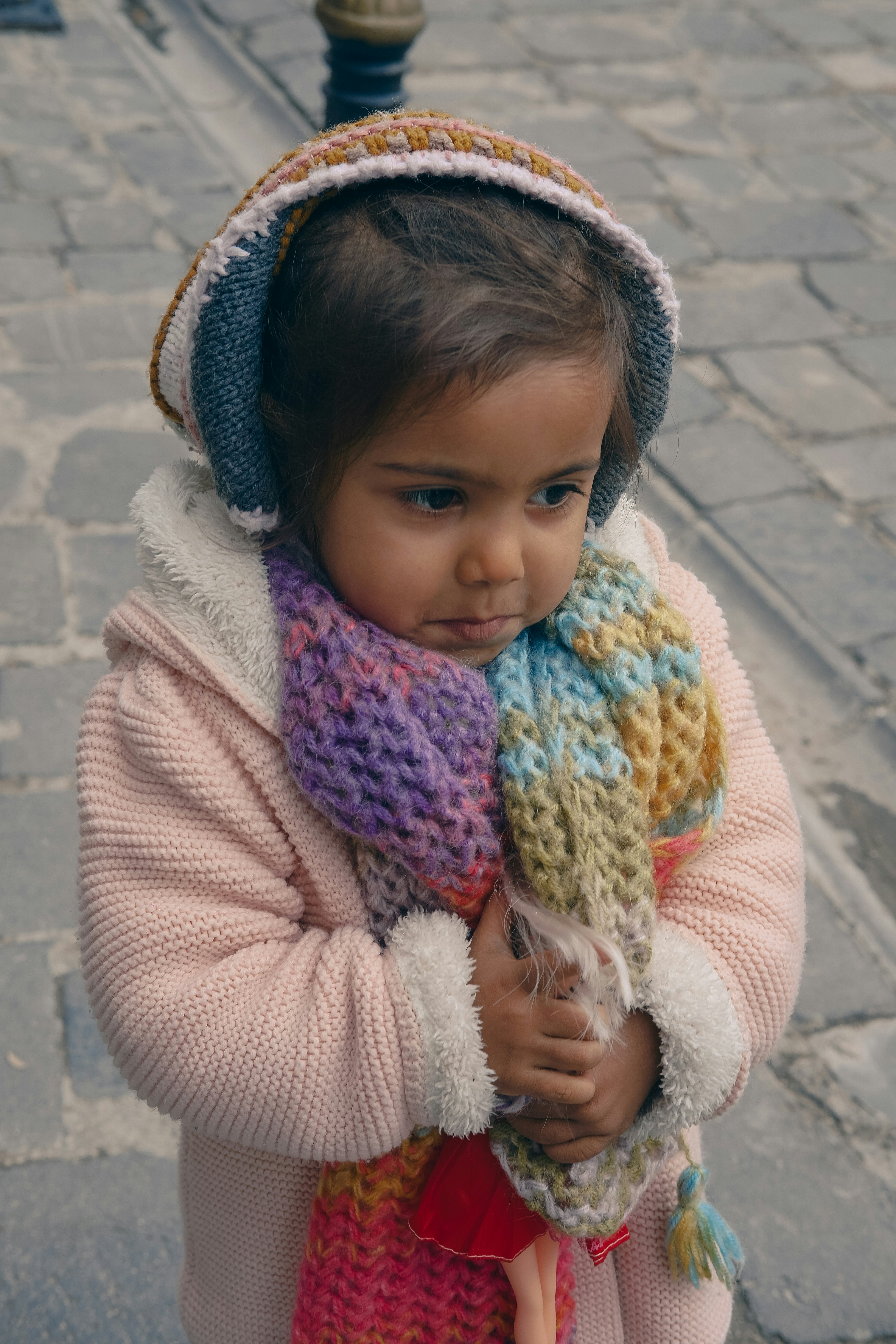 Soft-Collected Gaze: A Young Child in a Cozy Scarf on Cobblestones
