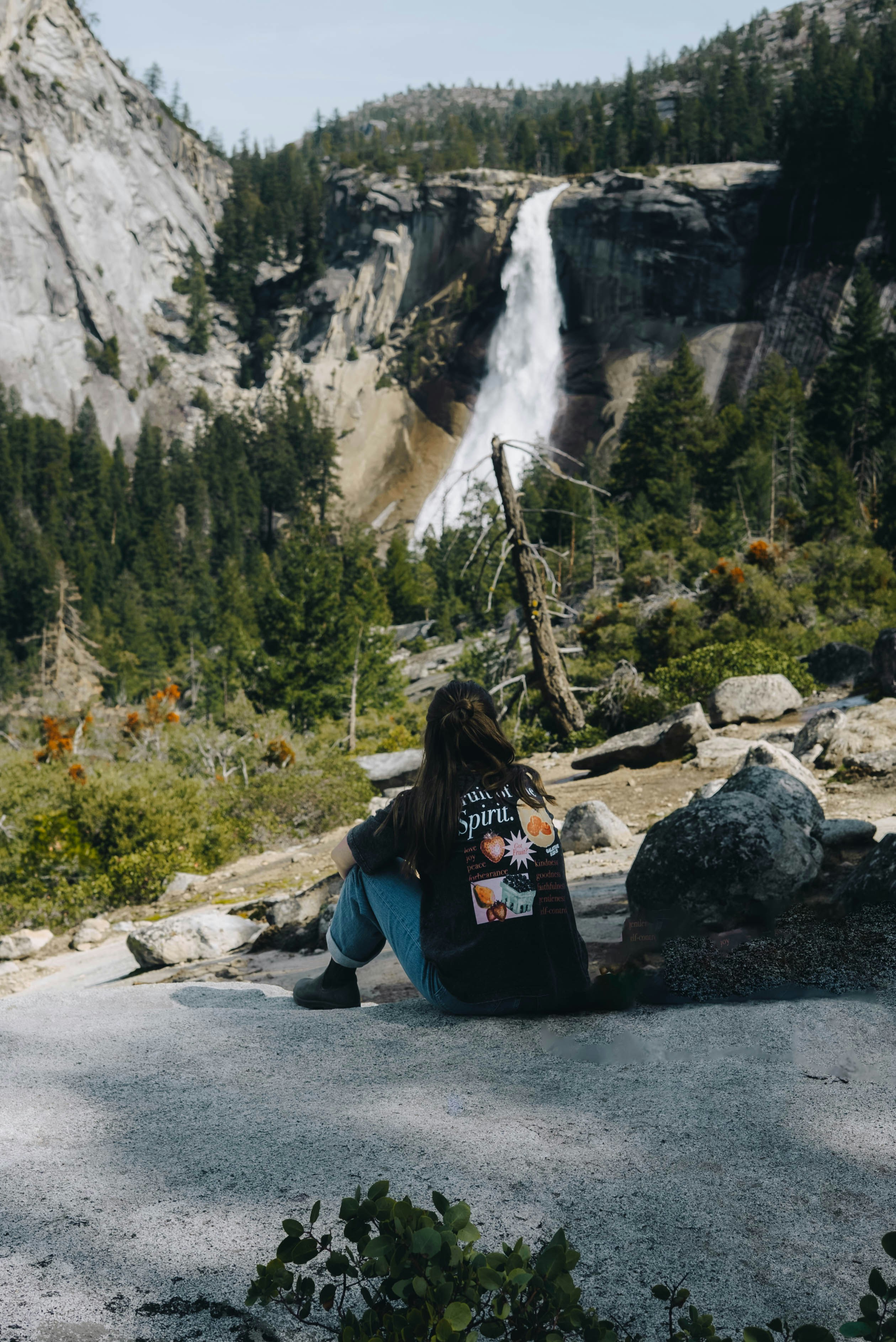 Woman sits watching a large waterfall in a rocky landscape.